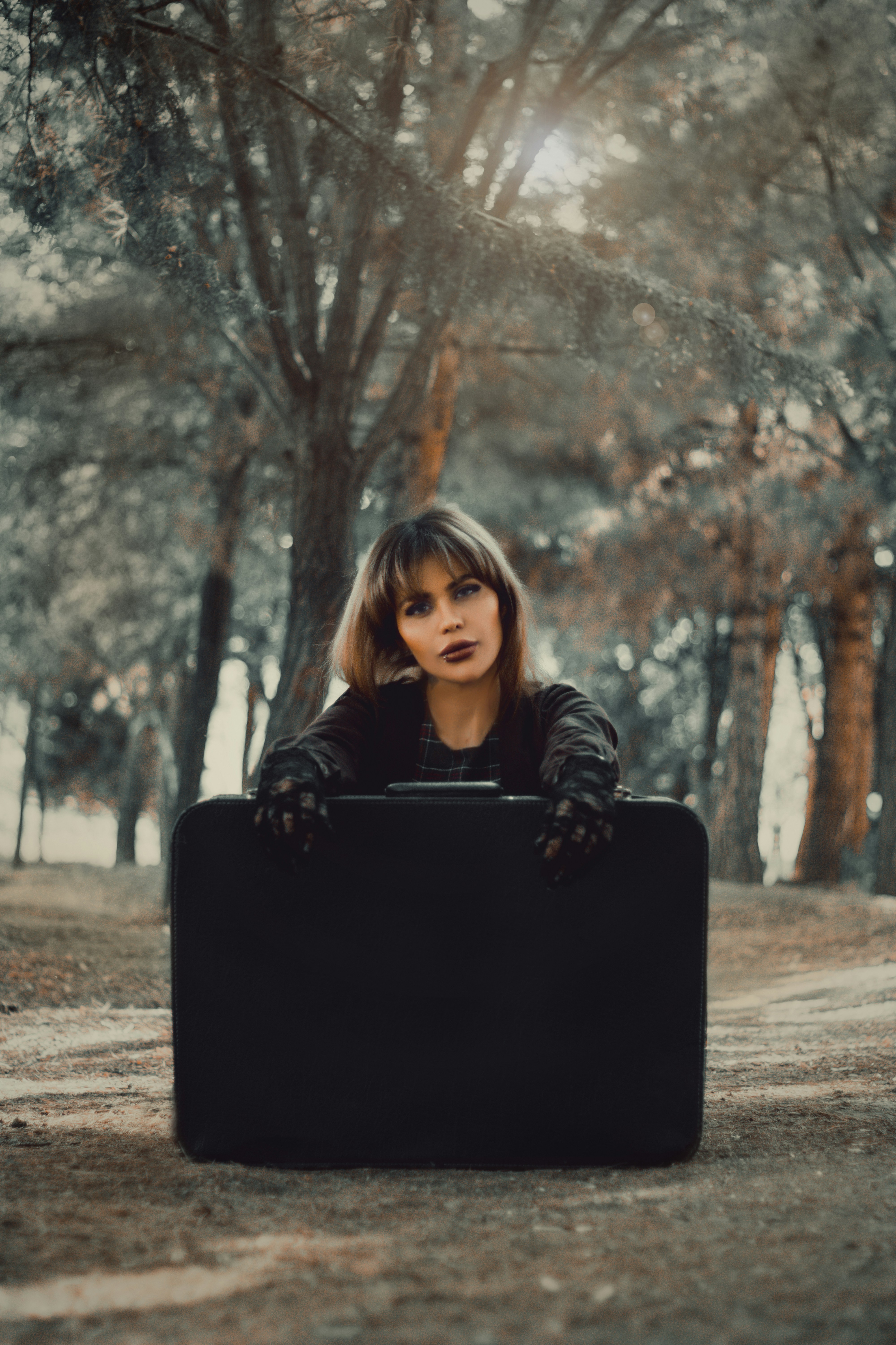 Quiet Edge: Portrait of a Woman with a Large Suitcase in a Dappled Forest