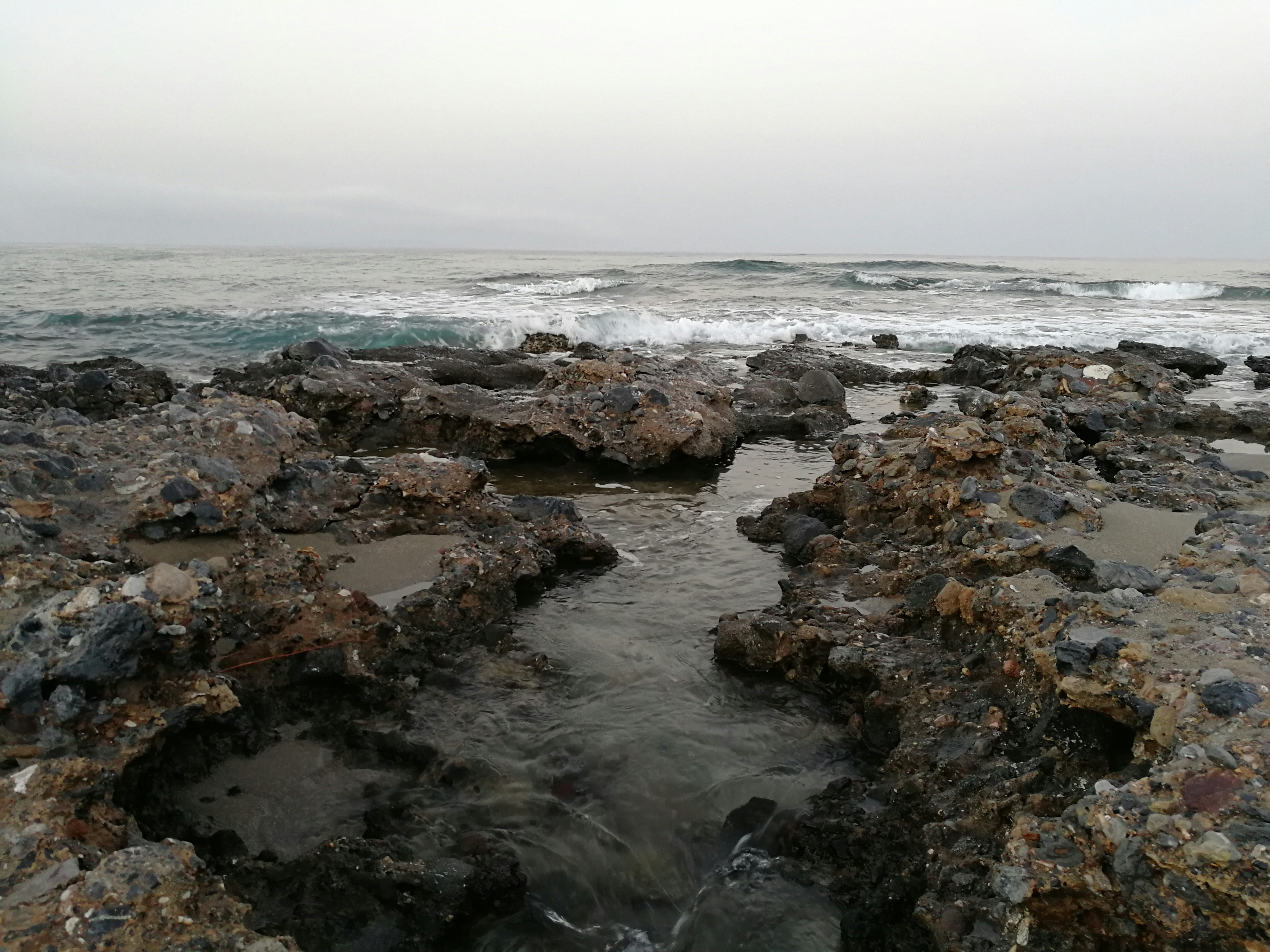 Rocky shoreline with tide pools reflecting the gentle waves under a cloudy sky.