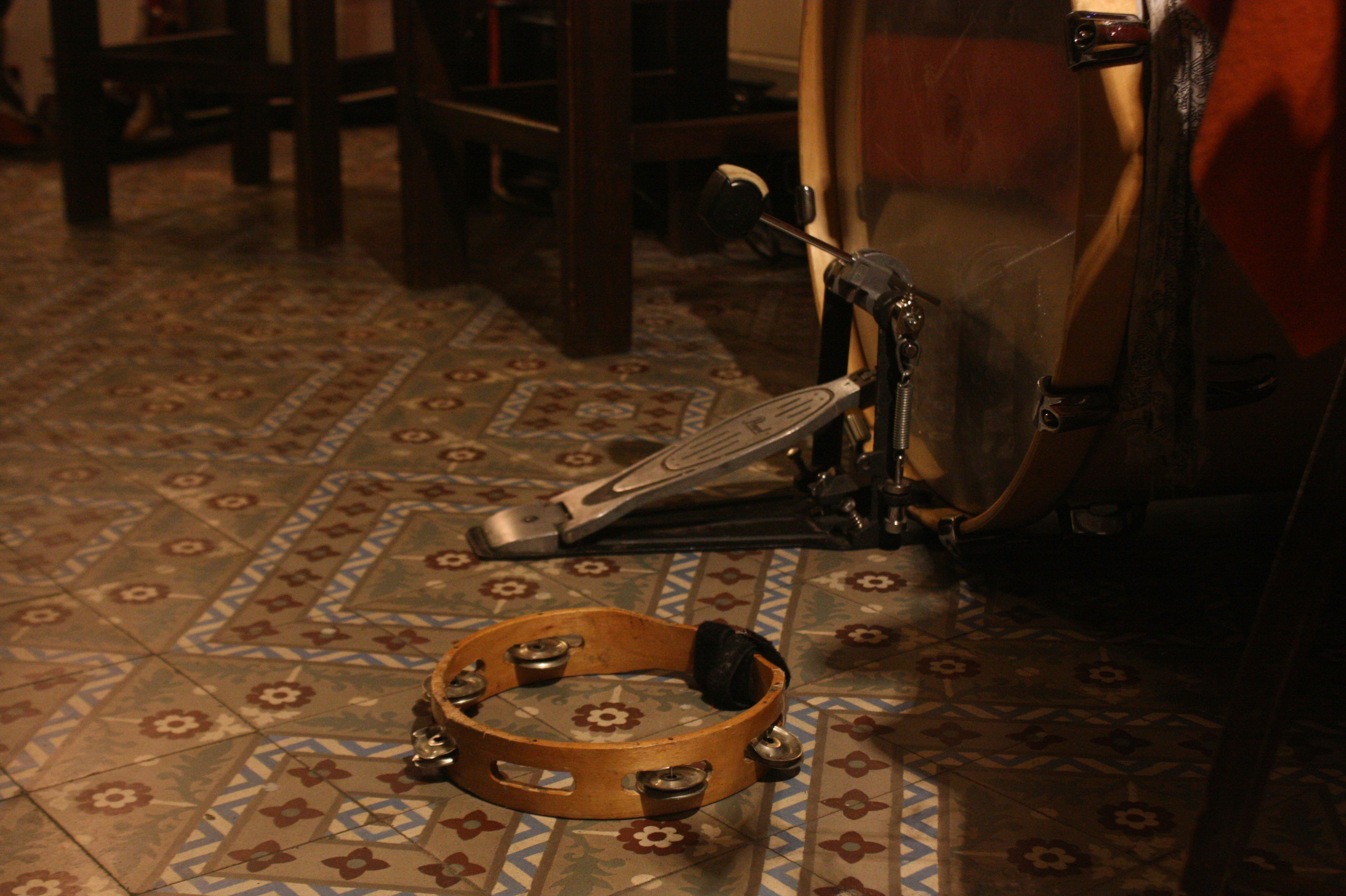 A tambourine rests on patterned floor tiles near a bass drum pedal, capturing the essence of a musical space.