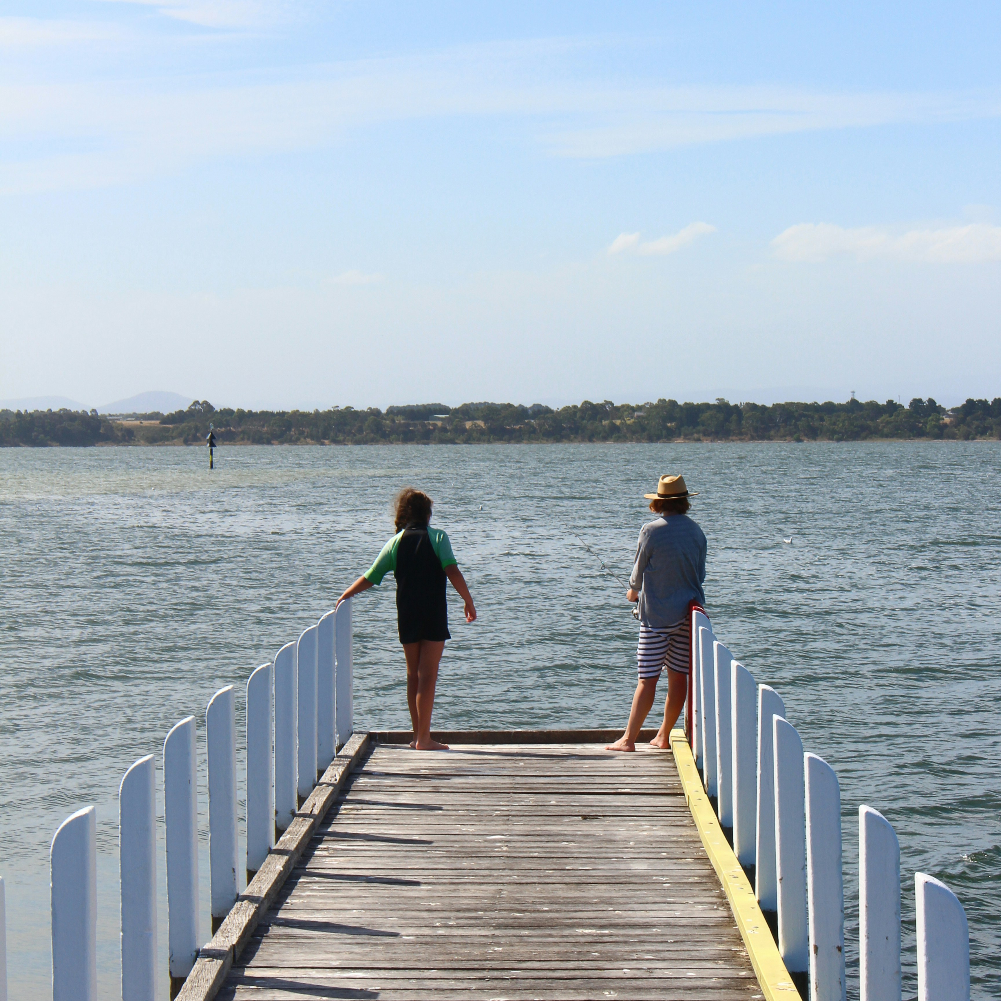 Two silhouettes at the end of a weathered pier on a calm bay