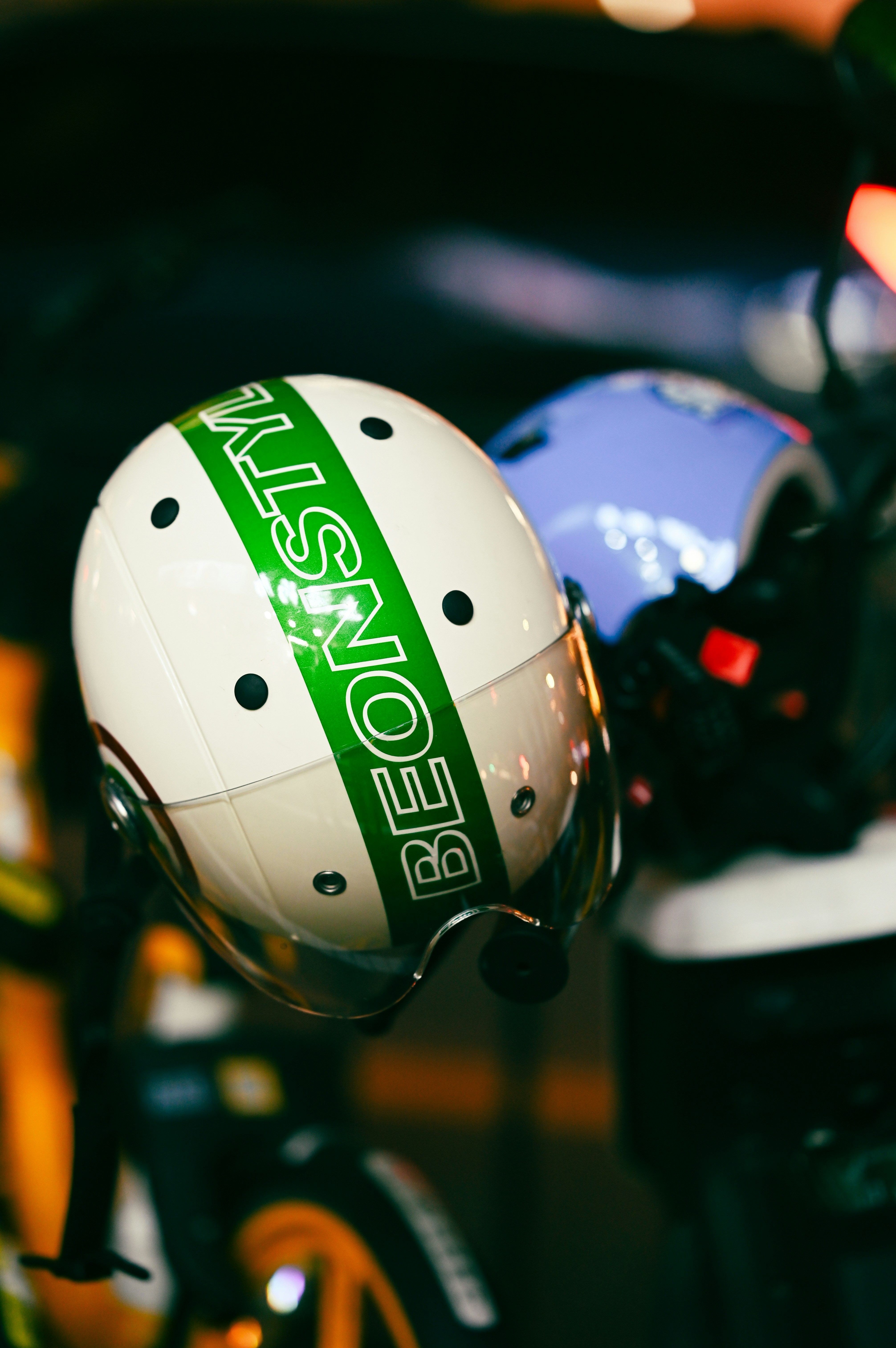 Close-up of a white racing helmet with green Beonton stripe in a dim showroom