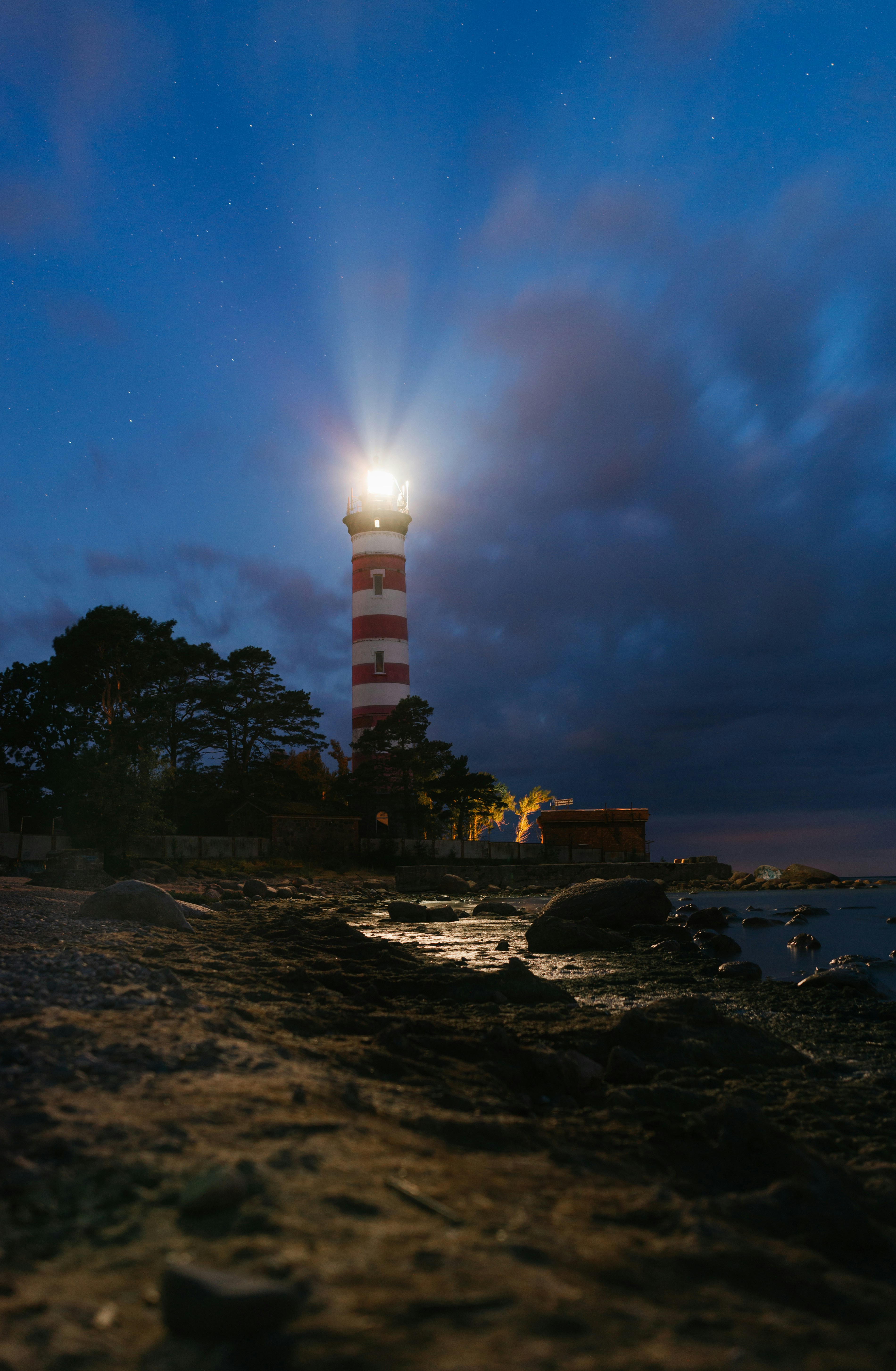 A lighthouse stands tall against a twilight sky, its beam cutting through the darkness and illuminating the rocky shoreline.