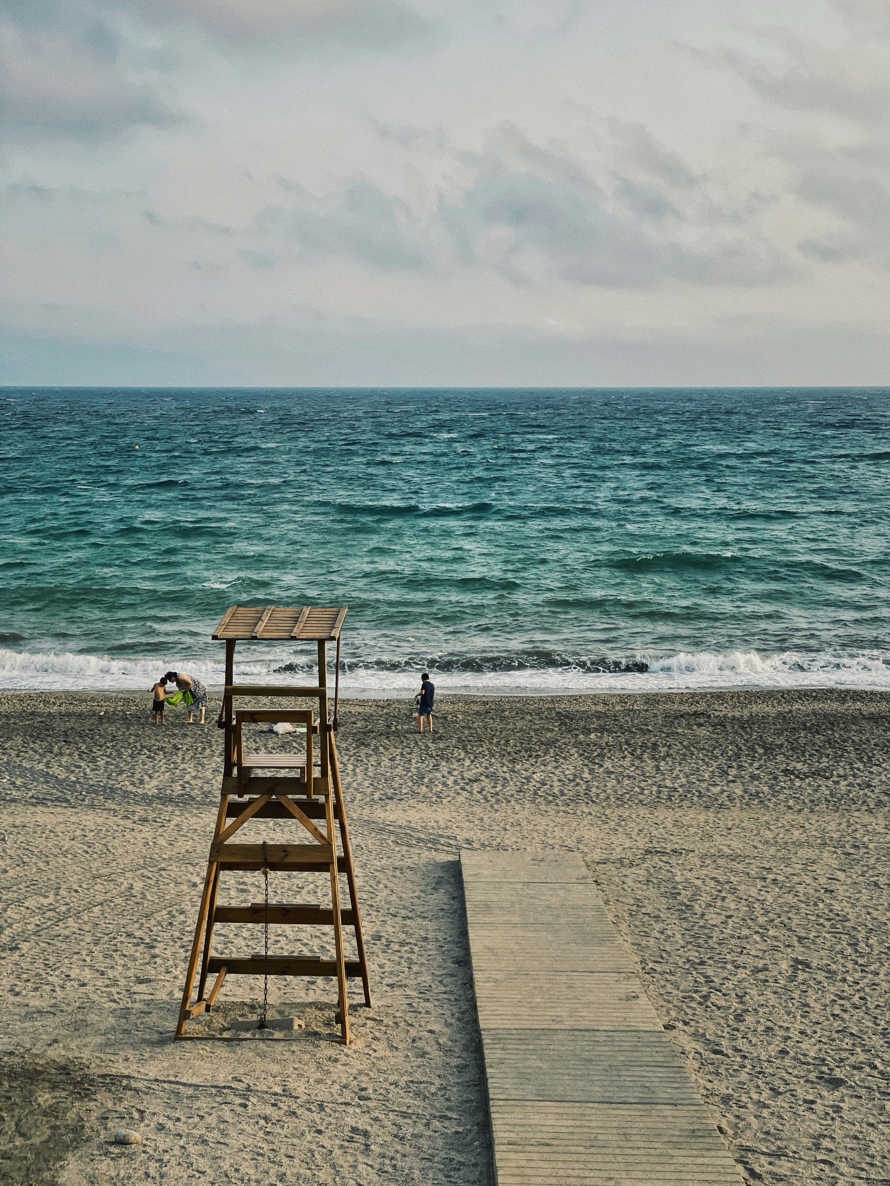 Wooden lifeguard tower overlooking a tranquil beach with people enjoying the ocean waves.