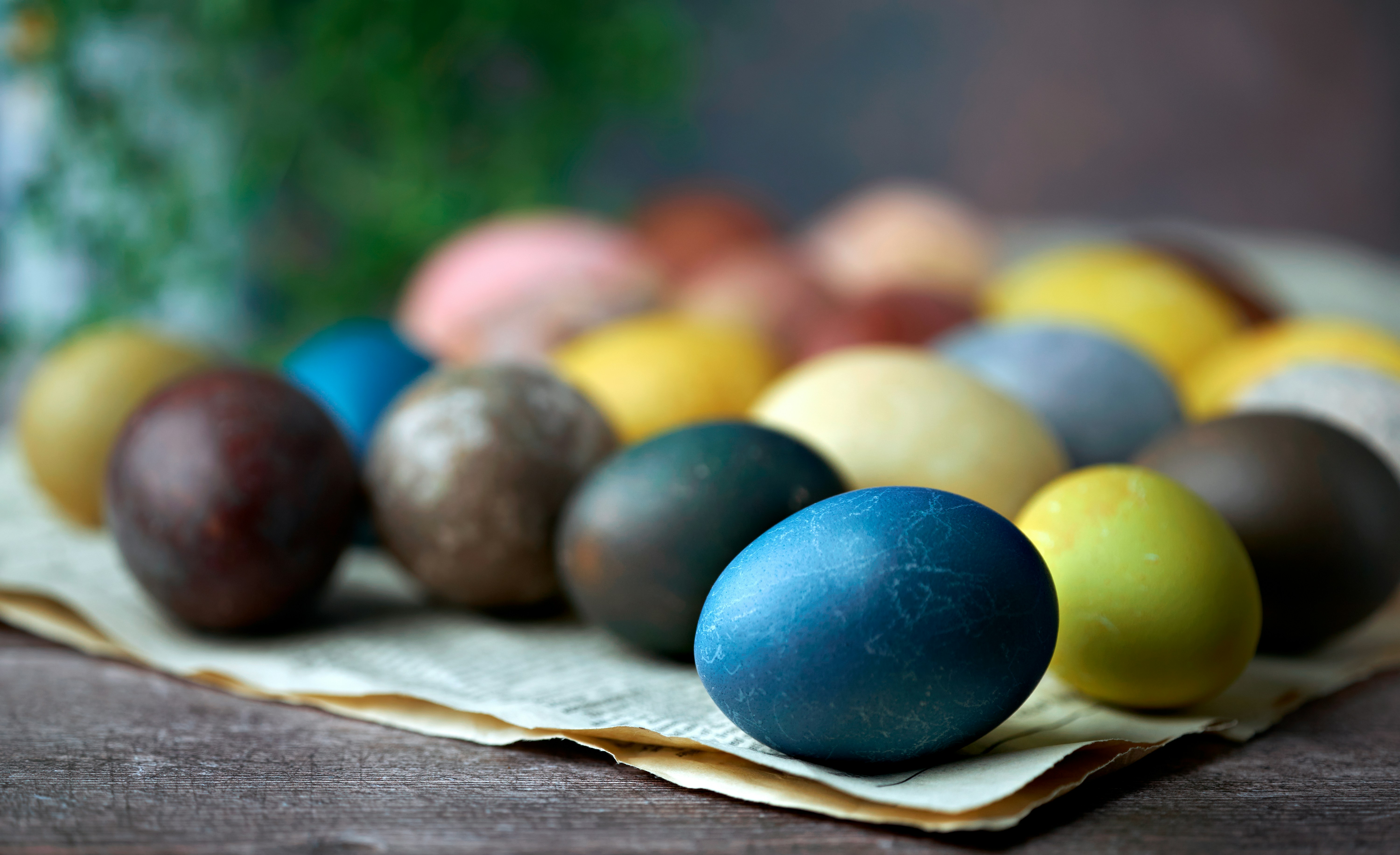 Colorful handcrafted Easter eggs arranged on a textured surface, showcasing a variety of hues and patterns. The background features soft greenery for added depth.