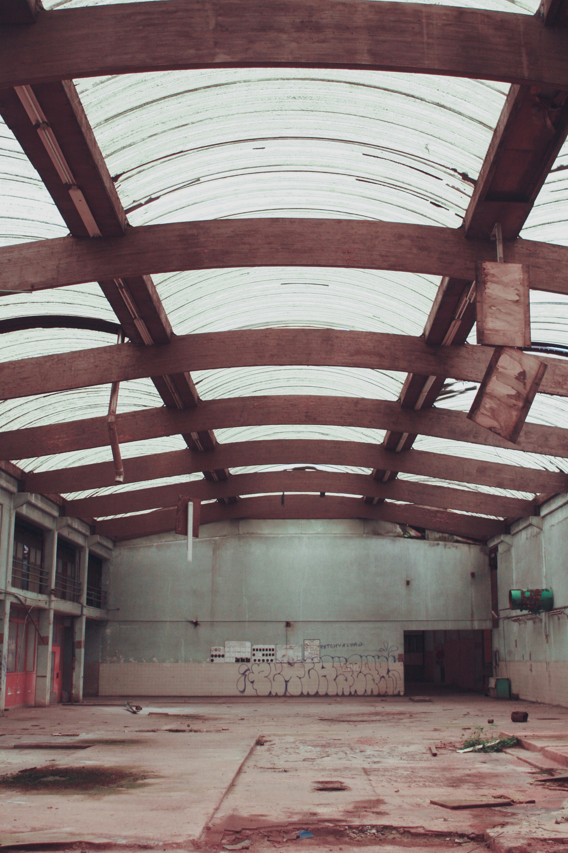 Interior of an abandoned building showcasing a curved wooden ceiling and remnants of graffiti on the walls.