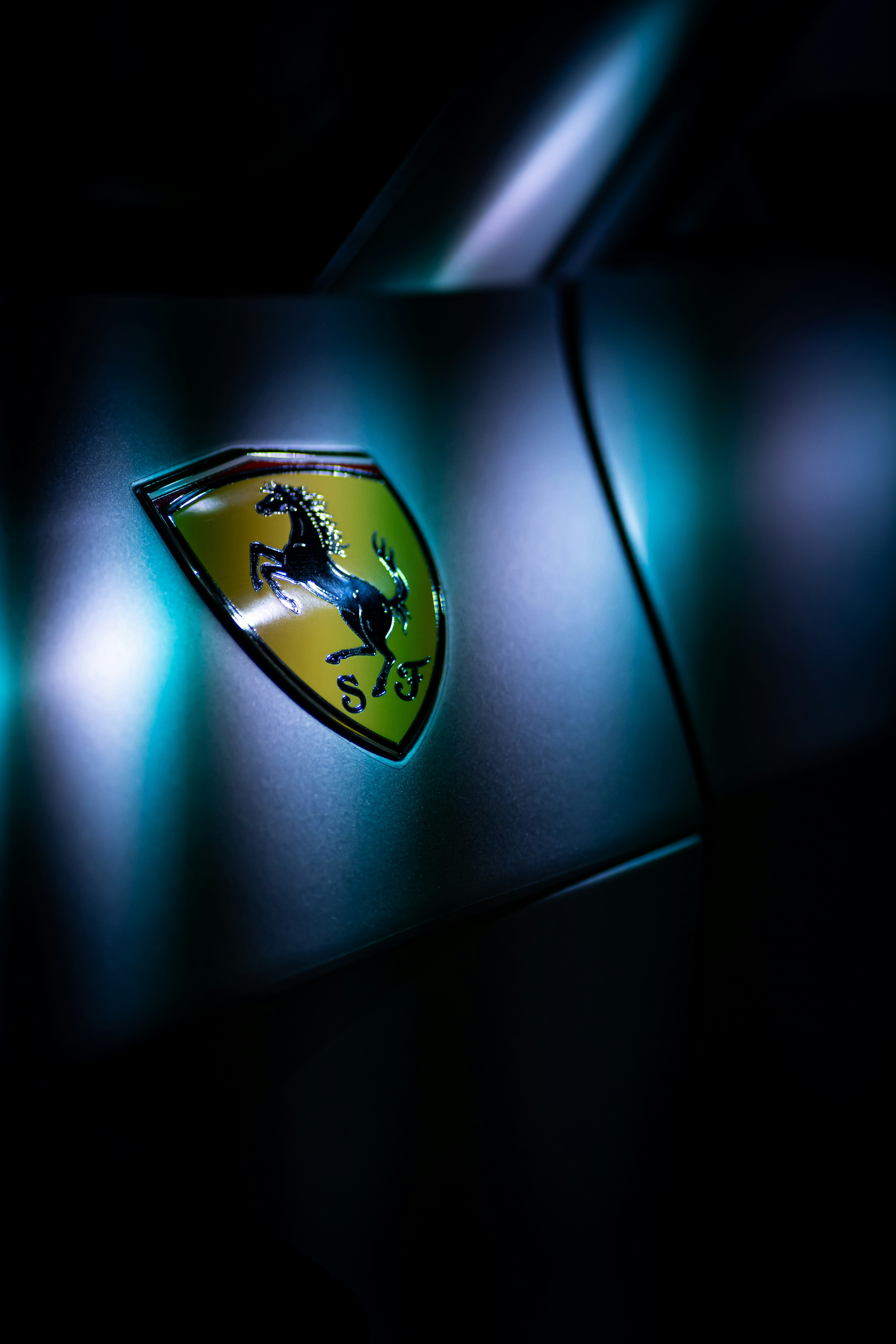 Close-up of a Ferrari emblem illuminated by soft lighting, highlighting its sleek design and iconic branding.