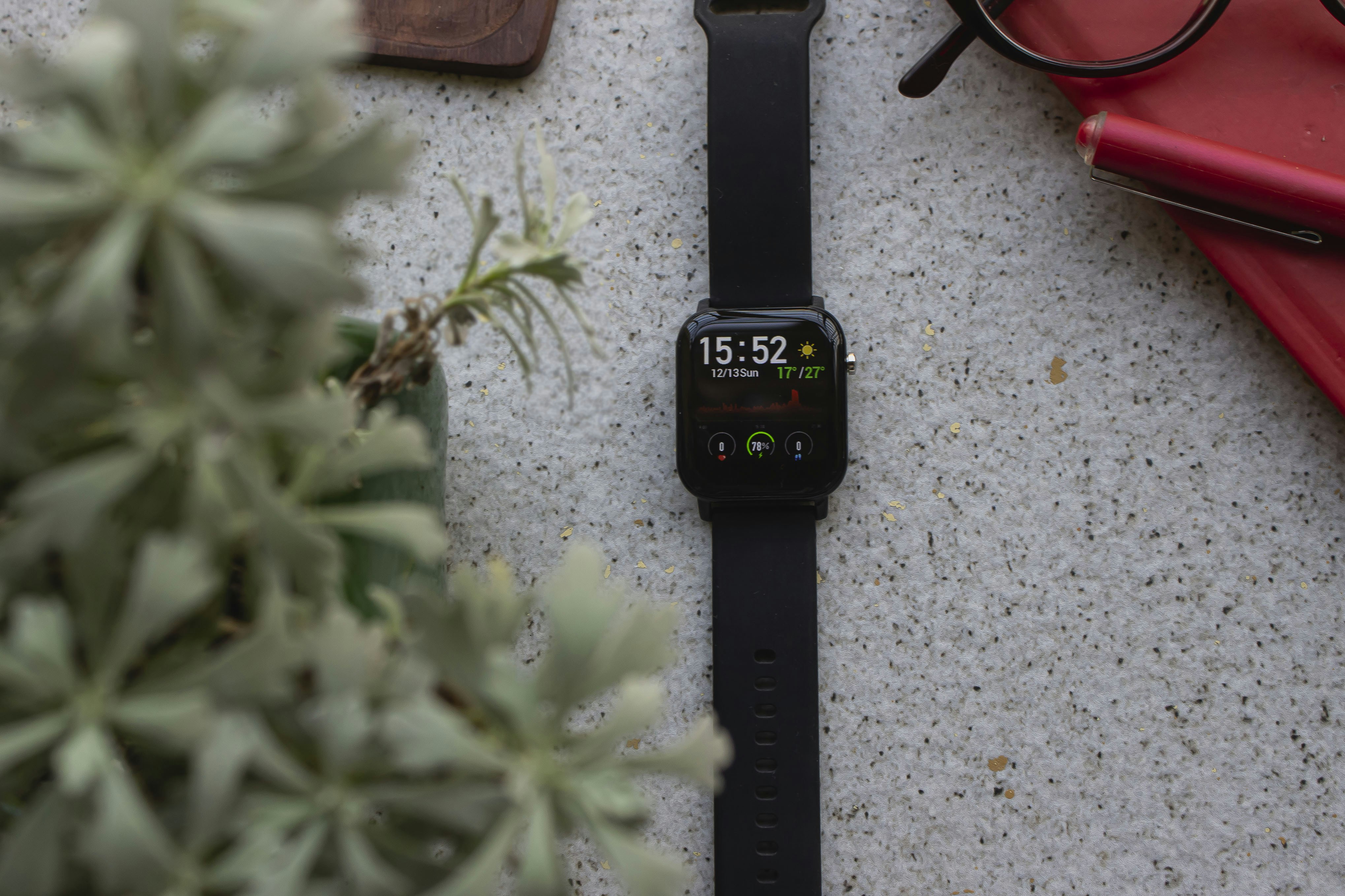 A smartwatch displaying the time and notifications, surrounded by greenery and stationery items on a textured surface.