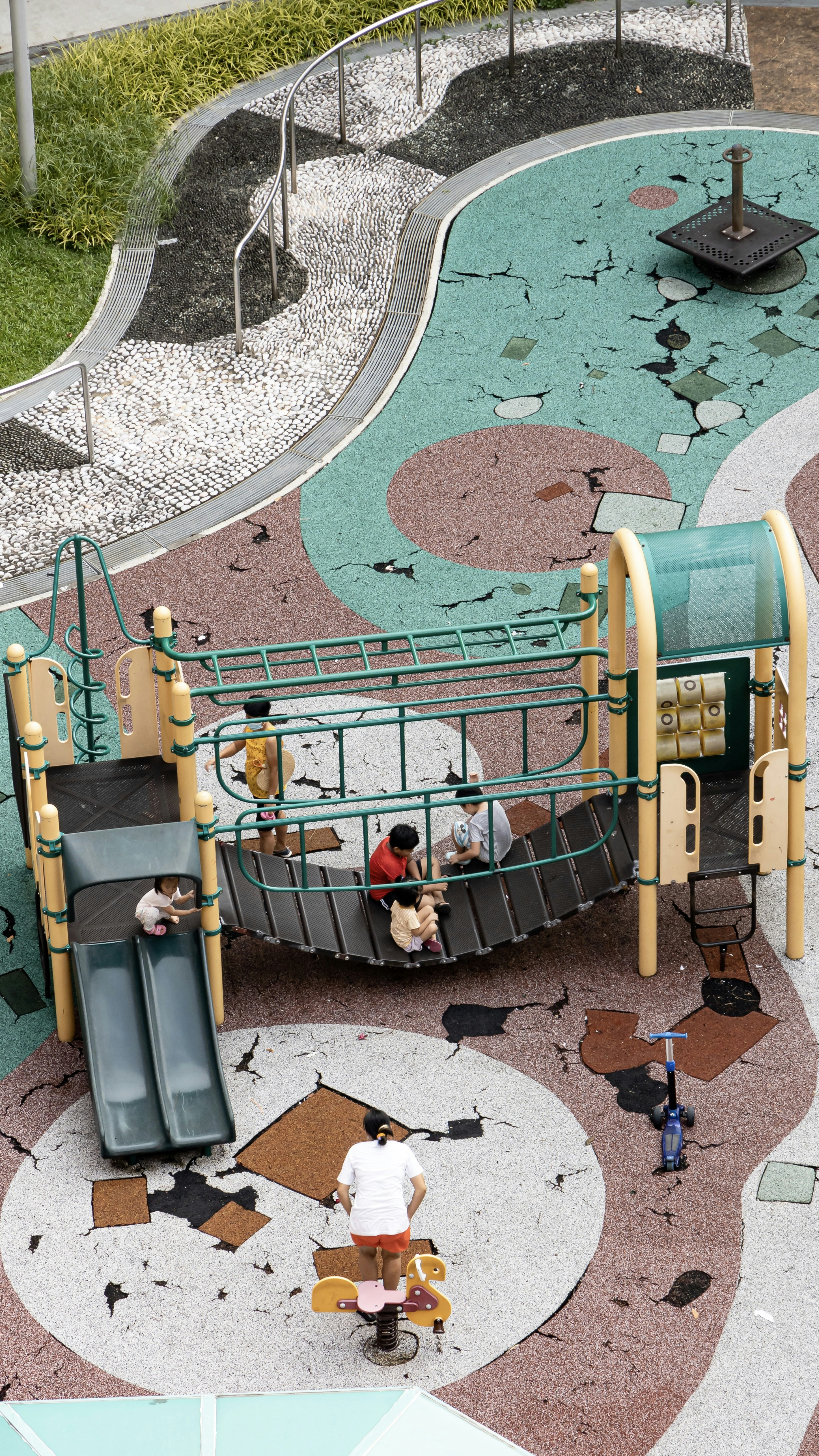 Children engaging in play on a vibrant playground, featuring slides and a unique floor design. A parent supervises from a distance.