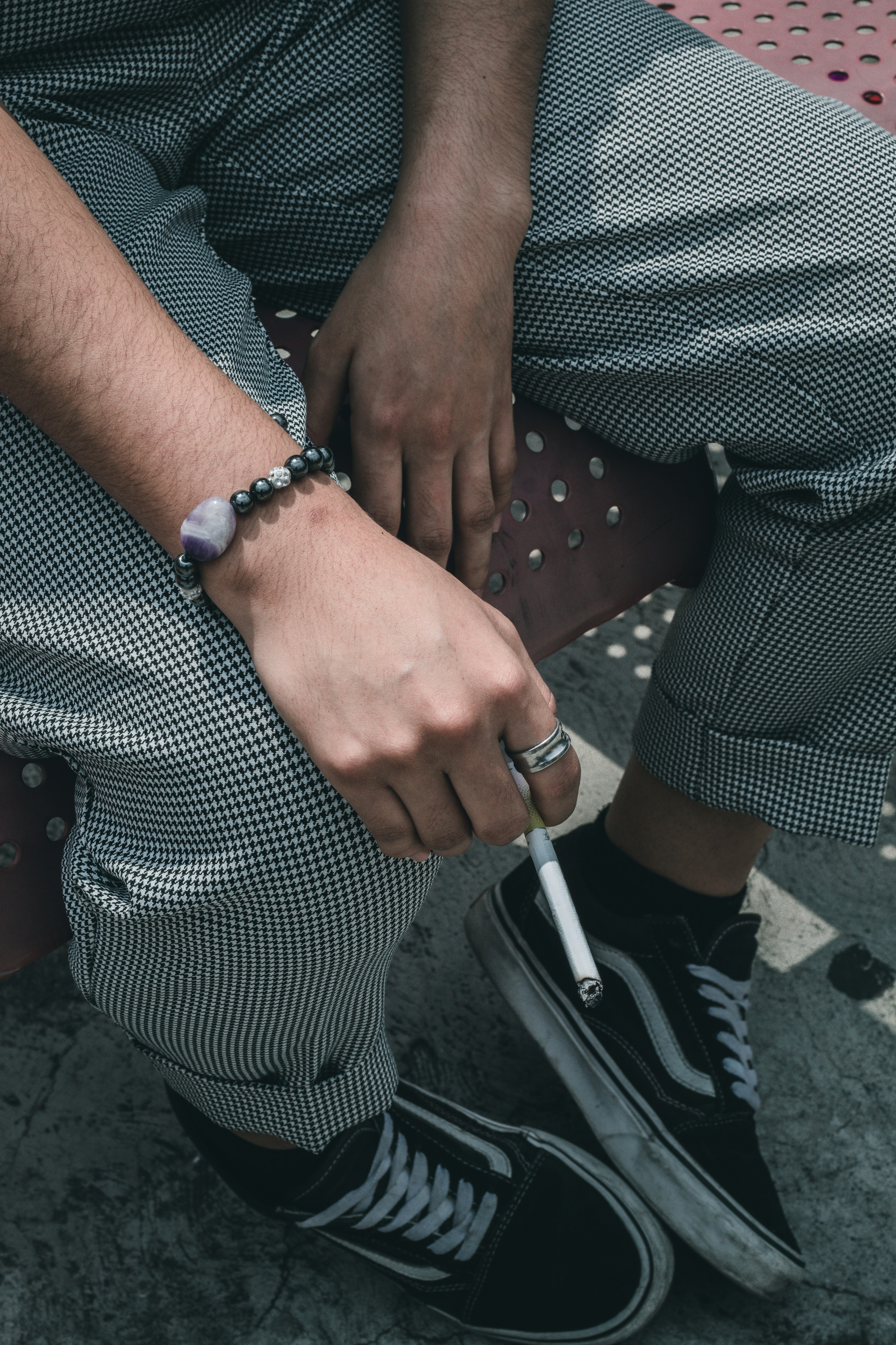 Close-up of a person's hand with a cigarette, adorned with bracelets, resting on a patterned surface. The focus highlights the contrast between urban life and personal moments.