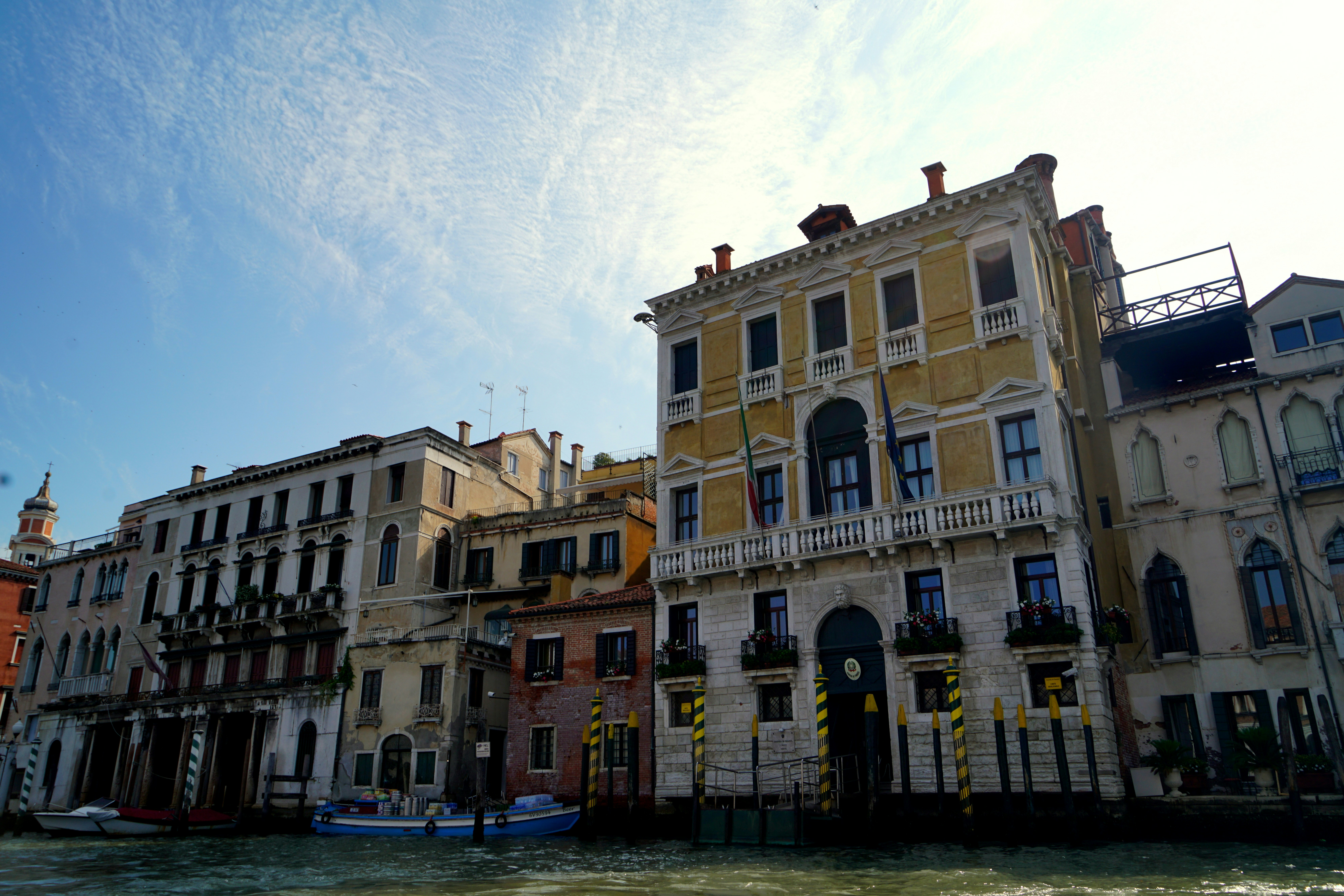 Historic Venetian buildings line the Grand Canal, showcasing intricate architecture and vibrant colors under a clear blue sky.