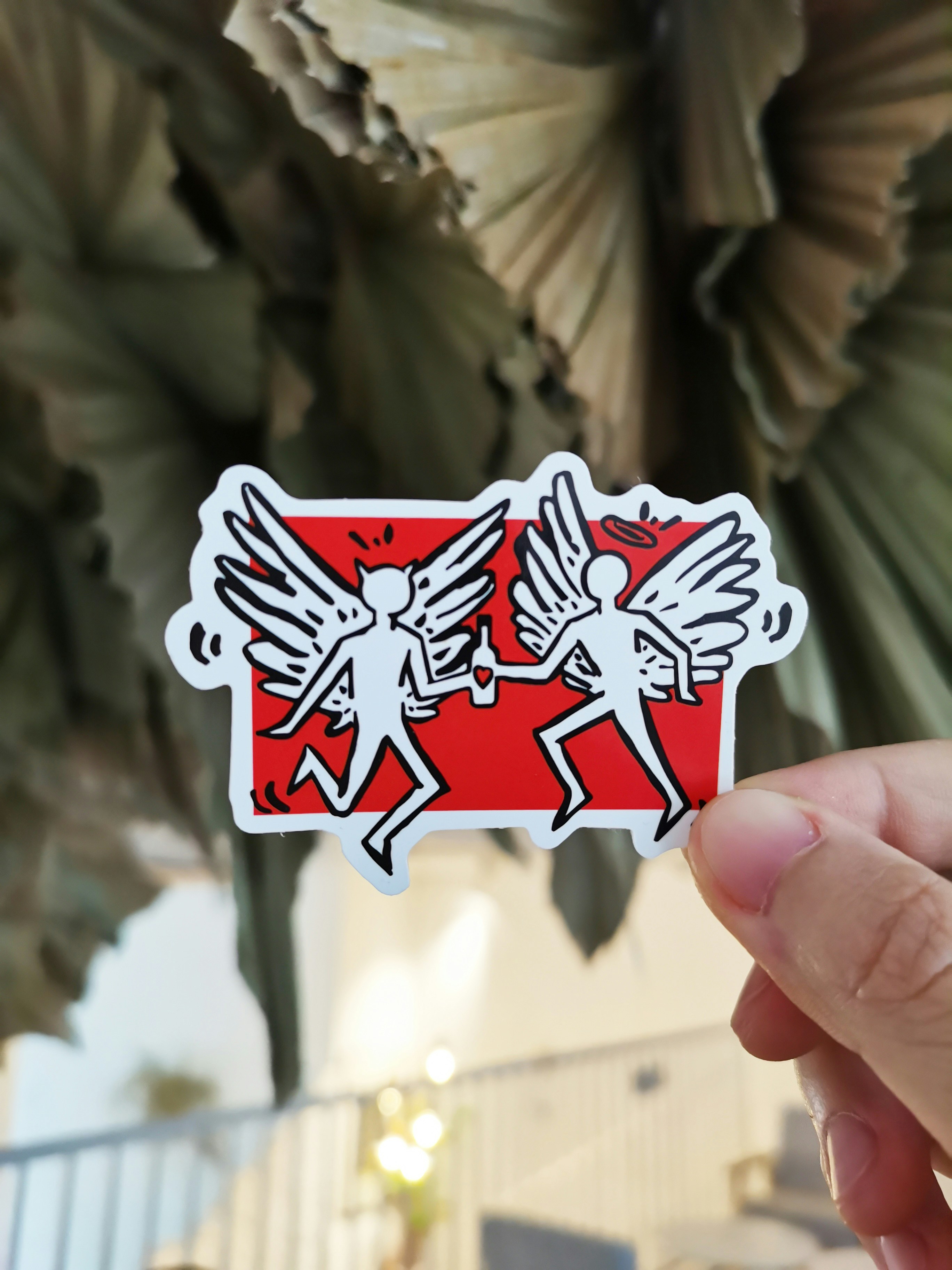 Winged Duo Sticker Held aloft Against Blurred Foliage