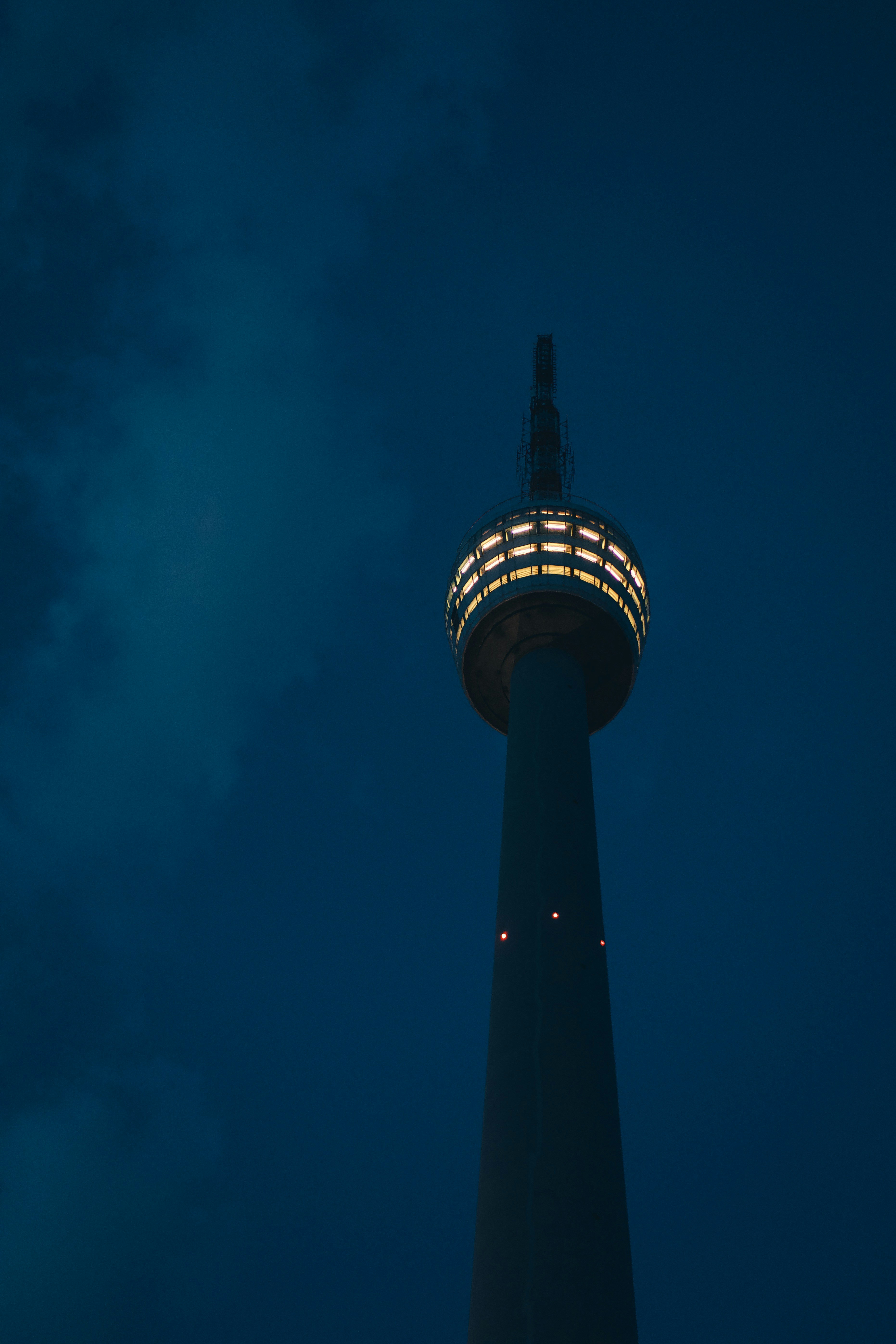 A tall communication tower illuminated against a darkening sky, showcasing its circular observation deck and antennae.