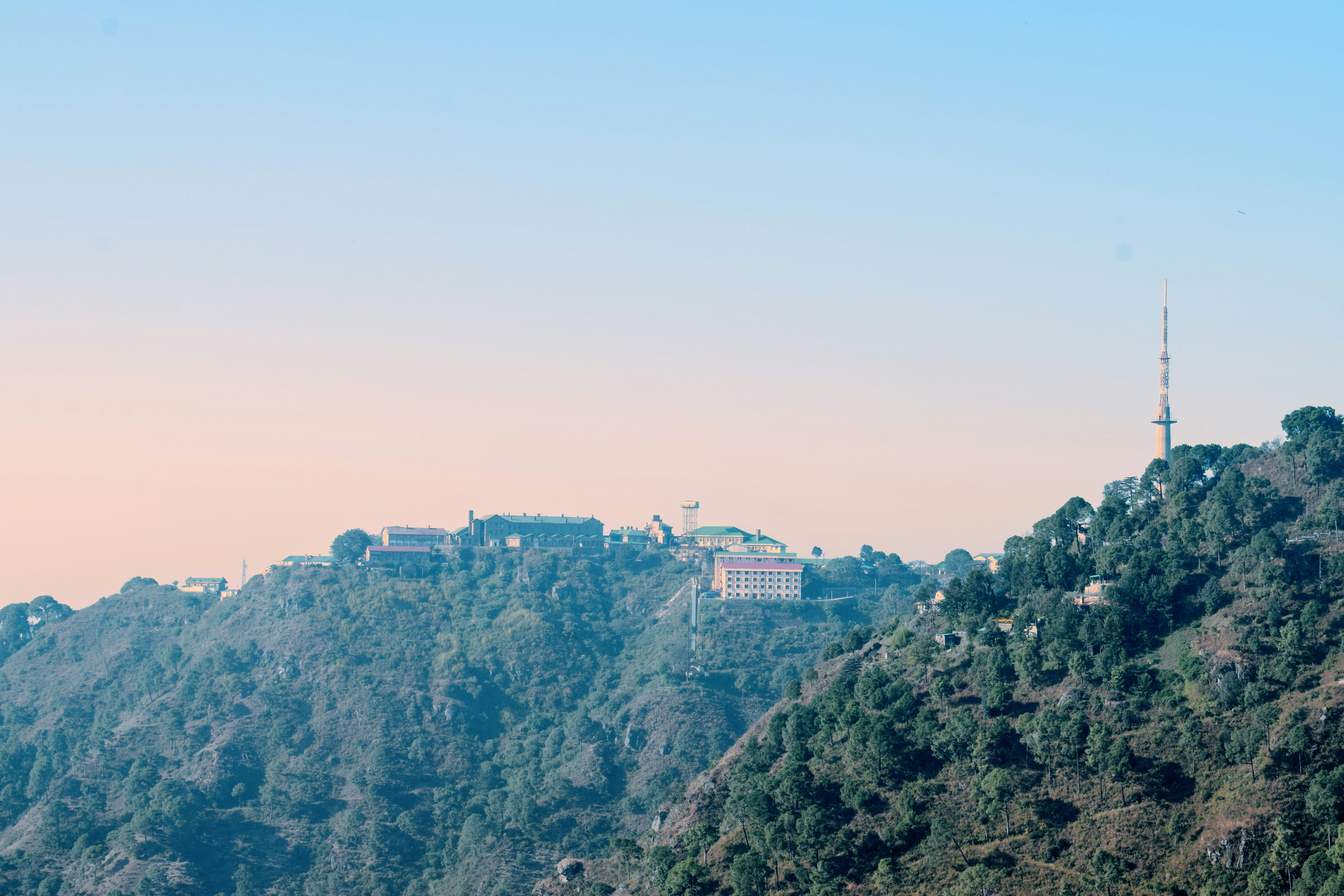 Historic buildings perched atop a lush hillside, framed by a clear sky and distant communication tower.