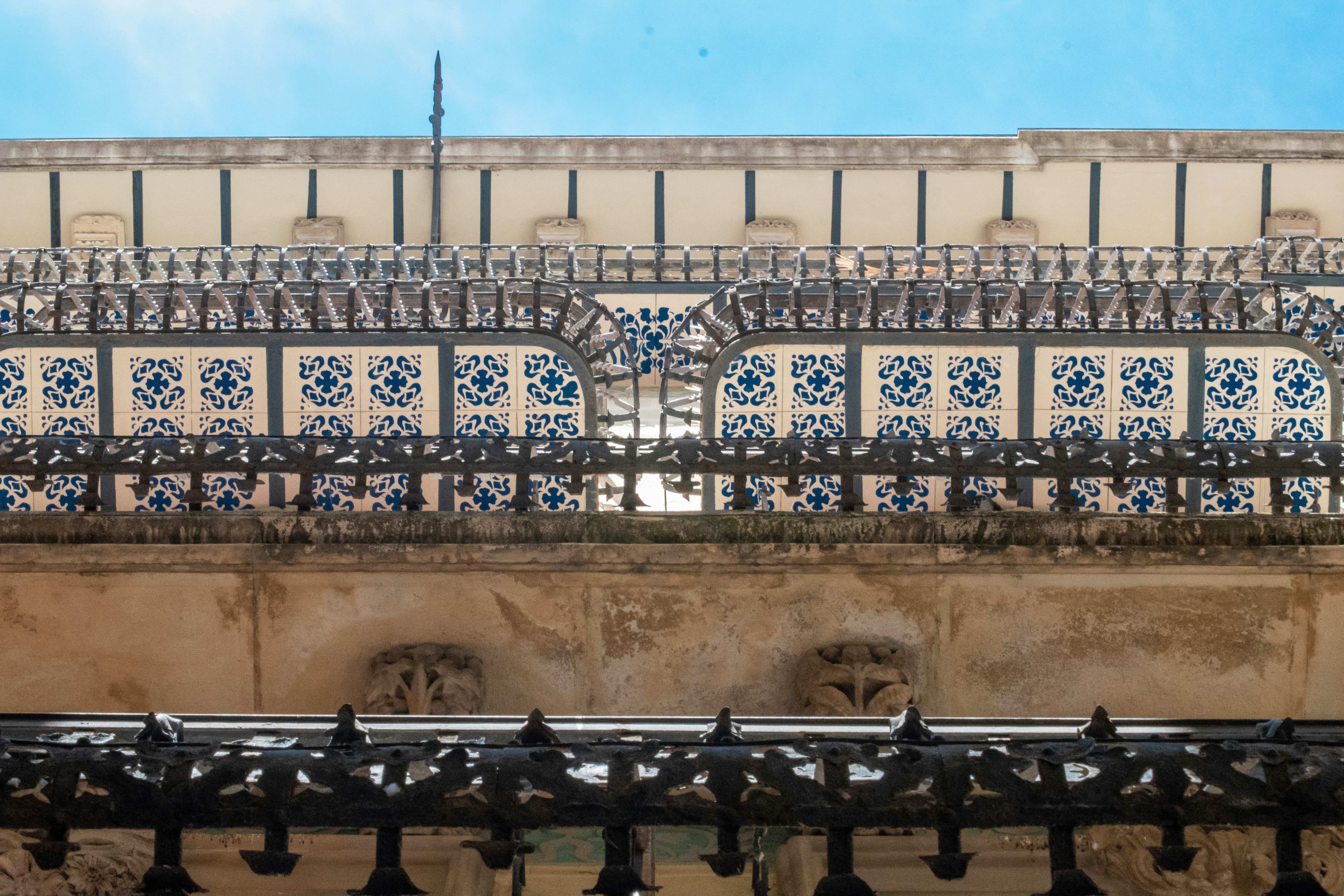 Wrought iron balcony with patterned tiles against a clear blue sky.