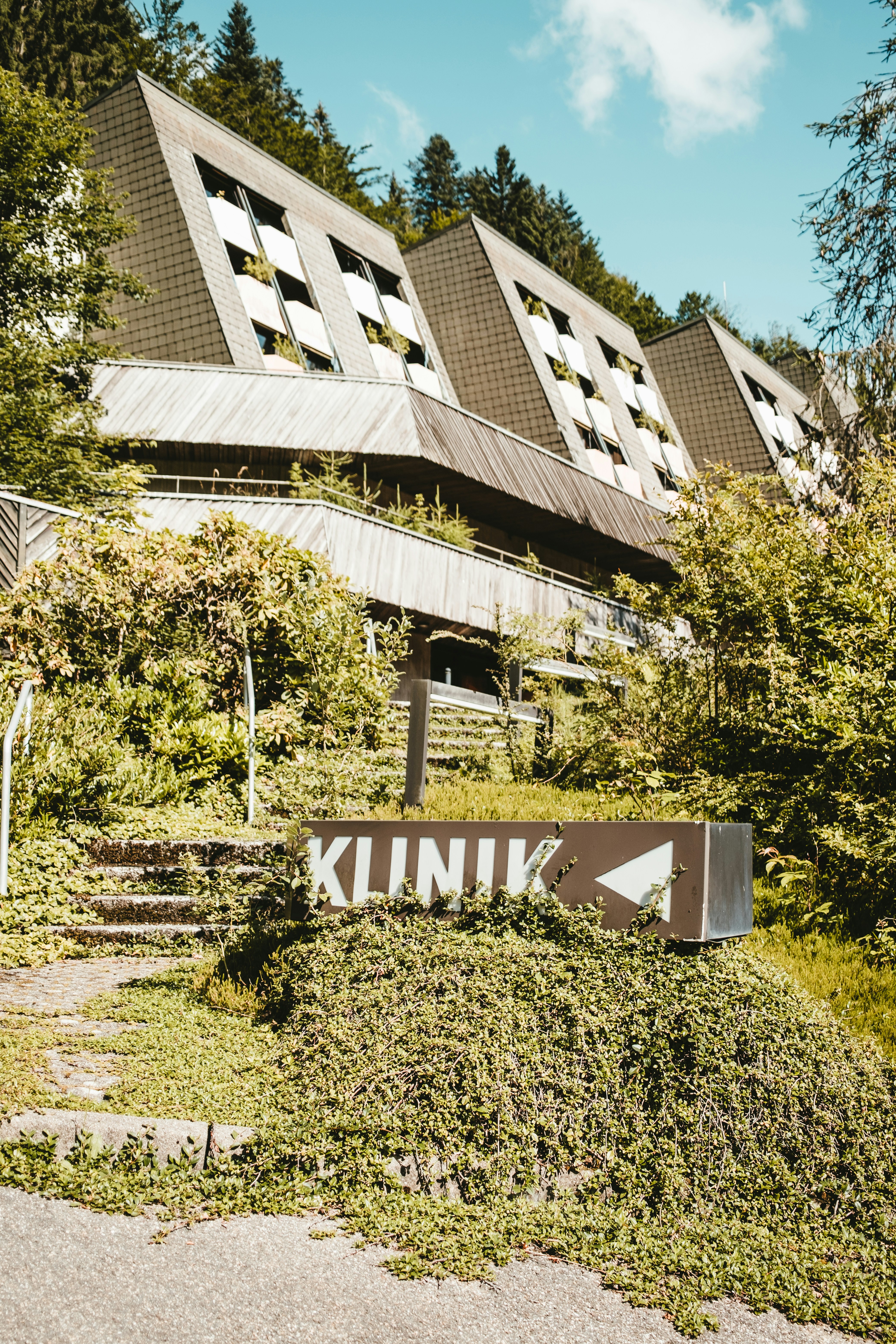 Sunlit Brutalism: Angular Facades and Verdant Encroachment