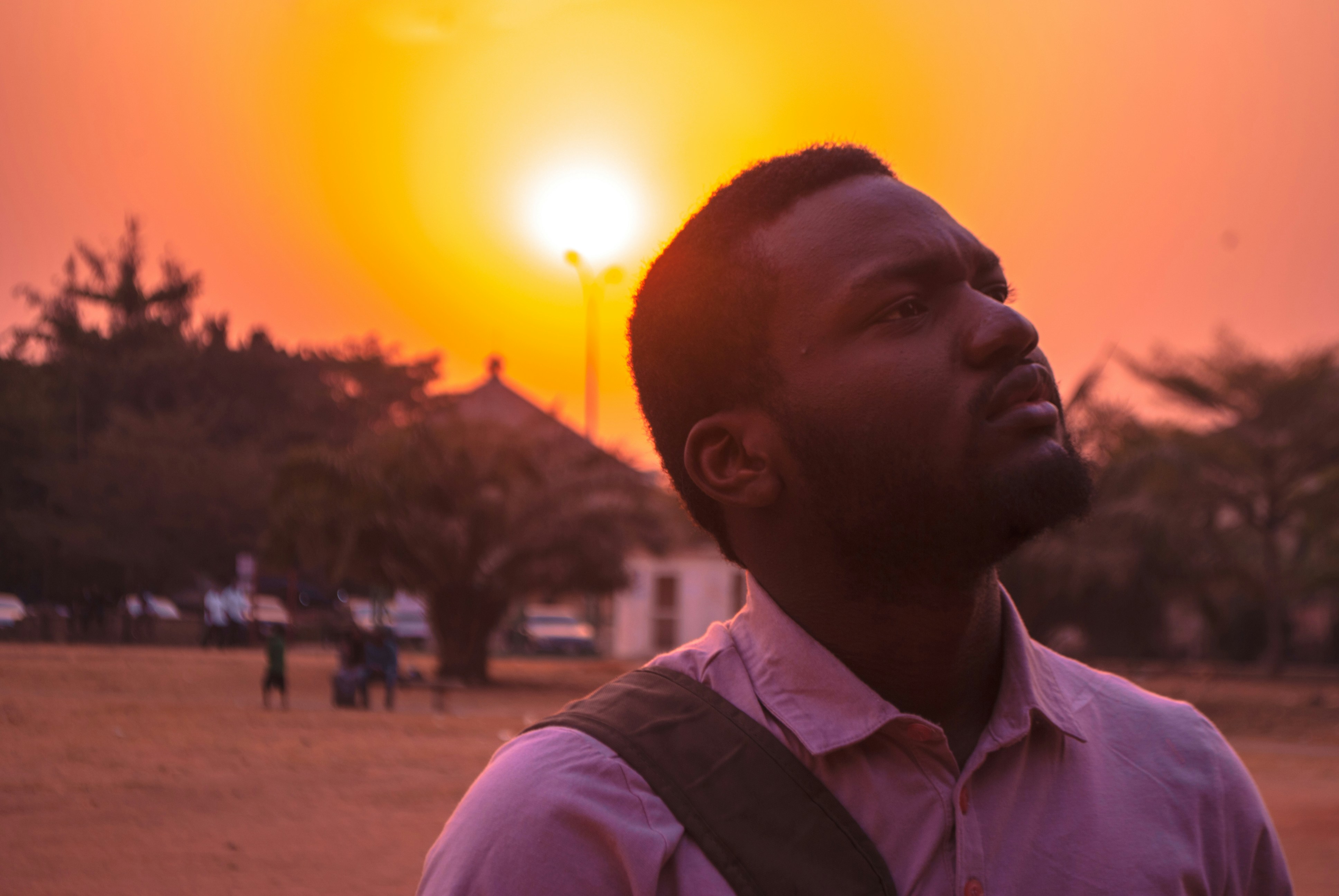 Silhouette of a man in a white shirt looking up against a vibrant orange sunset with trees in the background.