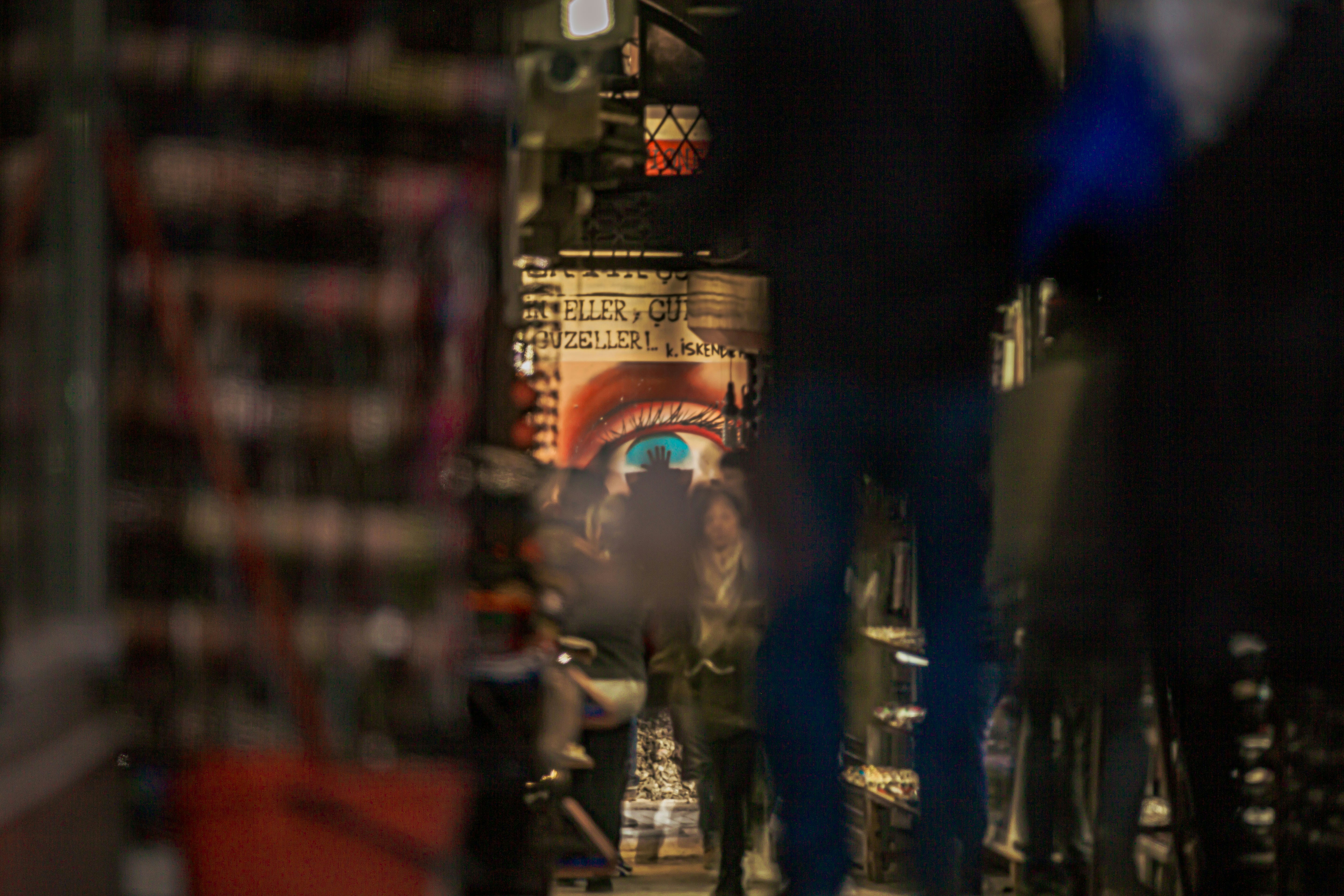 A blurred alleyway scene featuring an eye-catching mural at the end, surrounded by pedestrians. The composition evokes a sense of urban exploration.