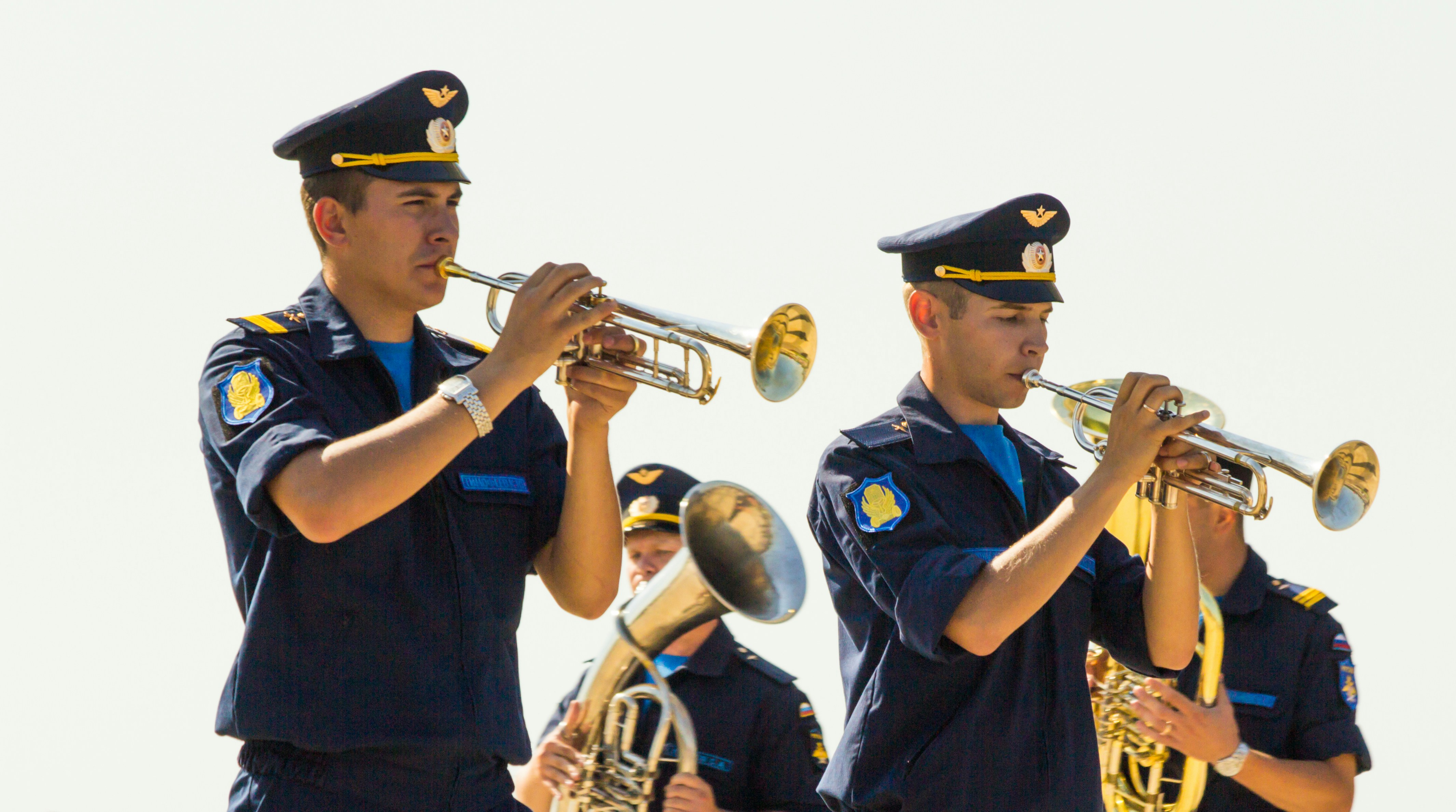 Musicians in uniform playing trumpets against a clear sky.