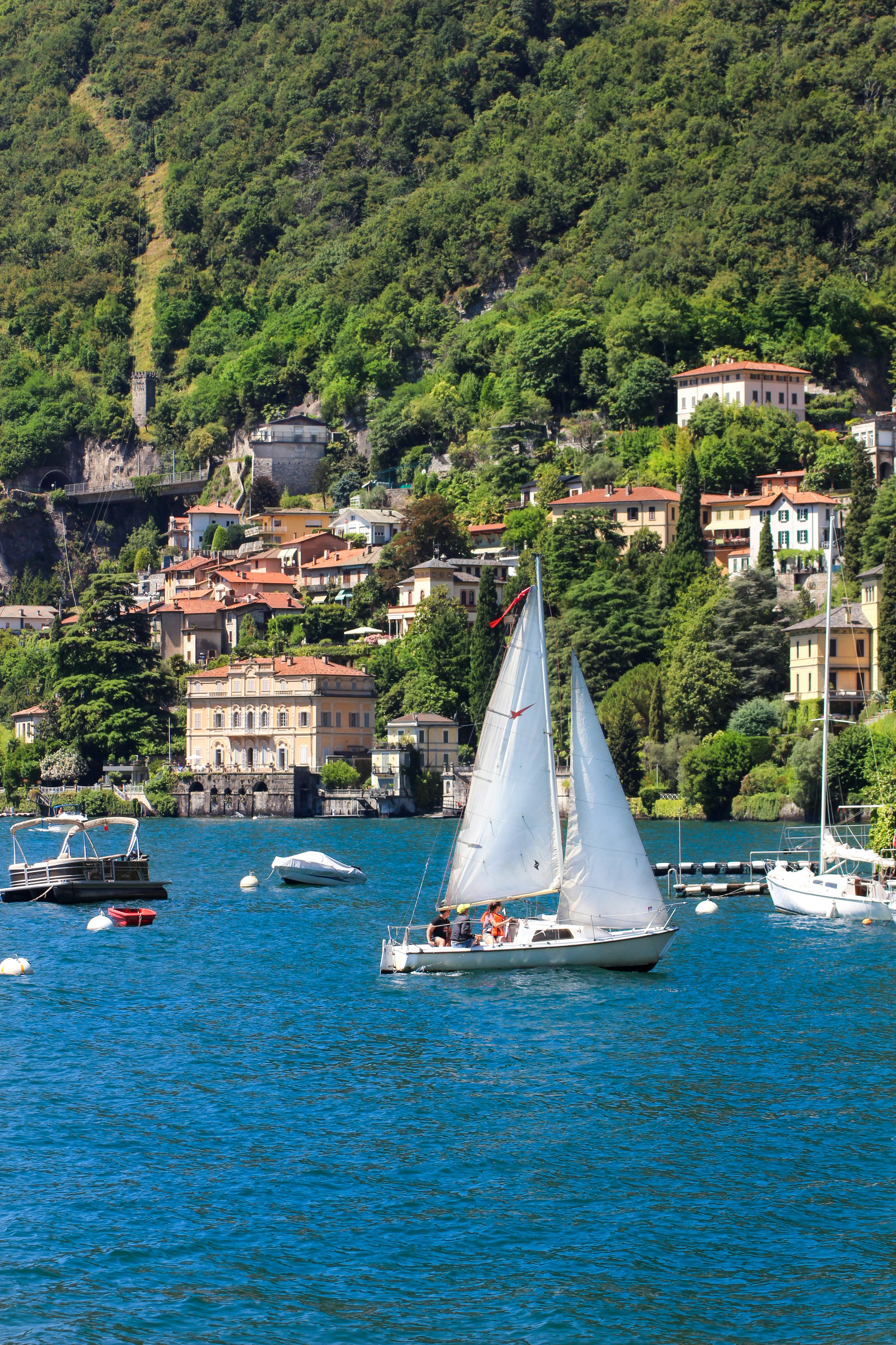 White sailboat gliding on Lake Como against a backdrop of lush green mountains and colorful hillside villas.