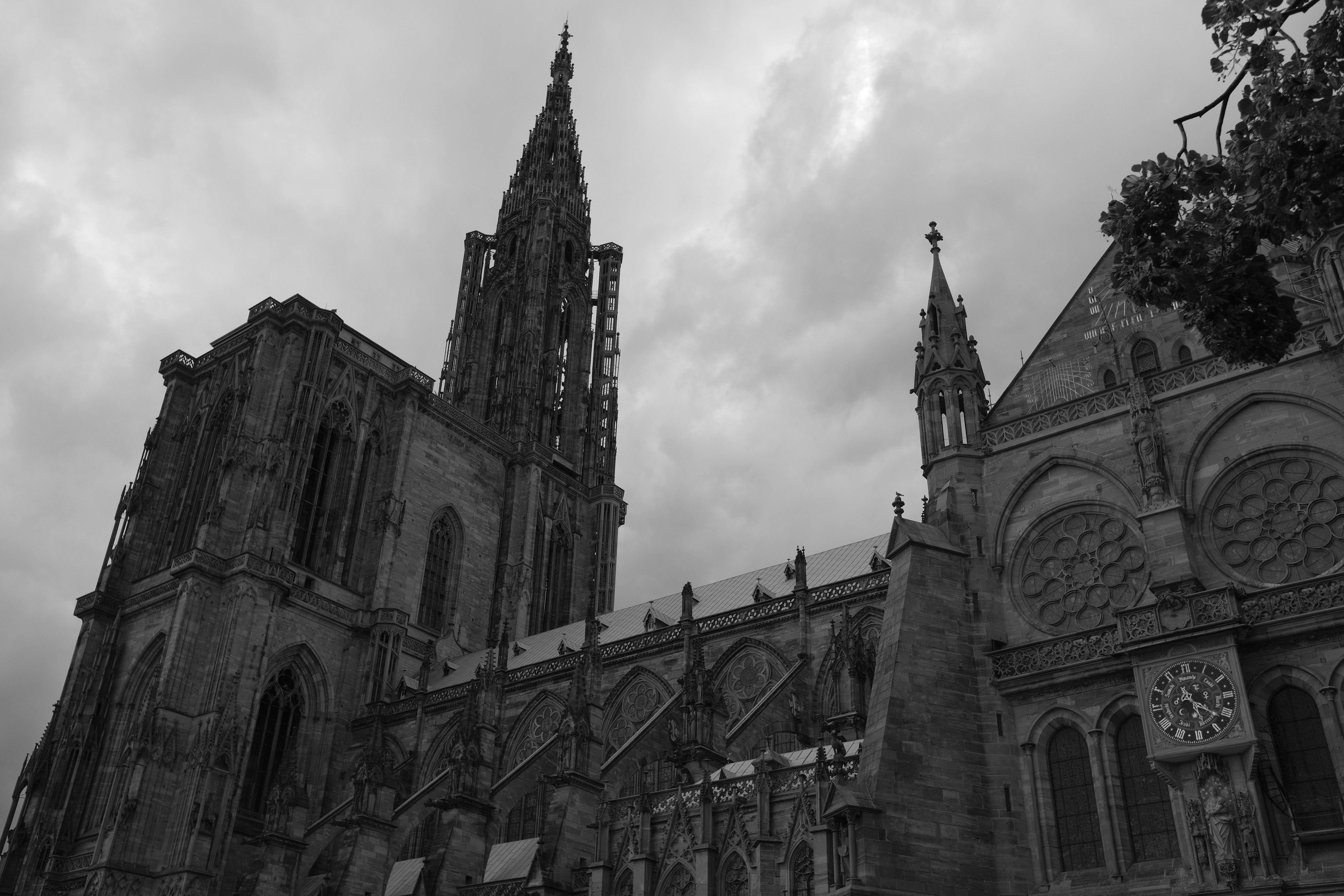 Grayscale view of an ornate Gothic cathedral facade with towering spires against a cloudy sky.
