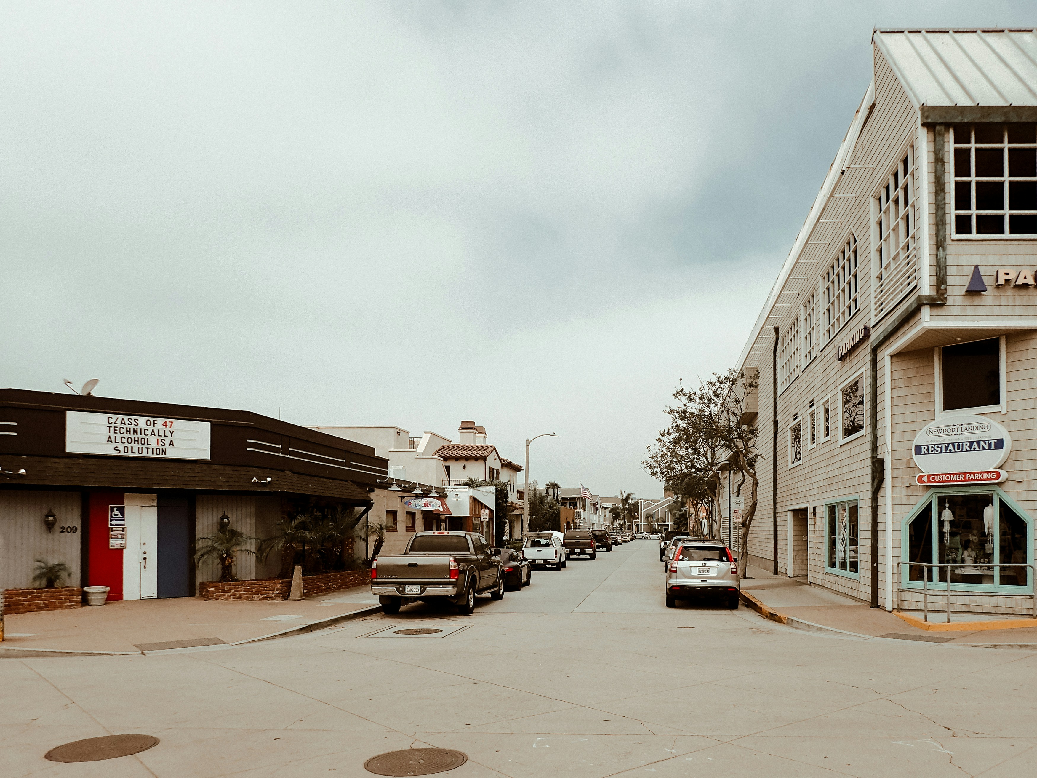 Charming coastal street scene featuring a mix of shops and parked vehicles under an overcast sky.