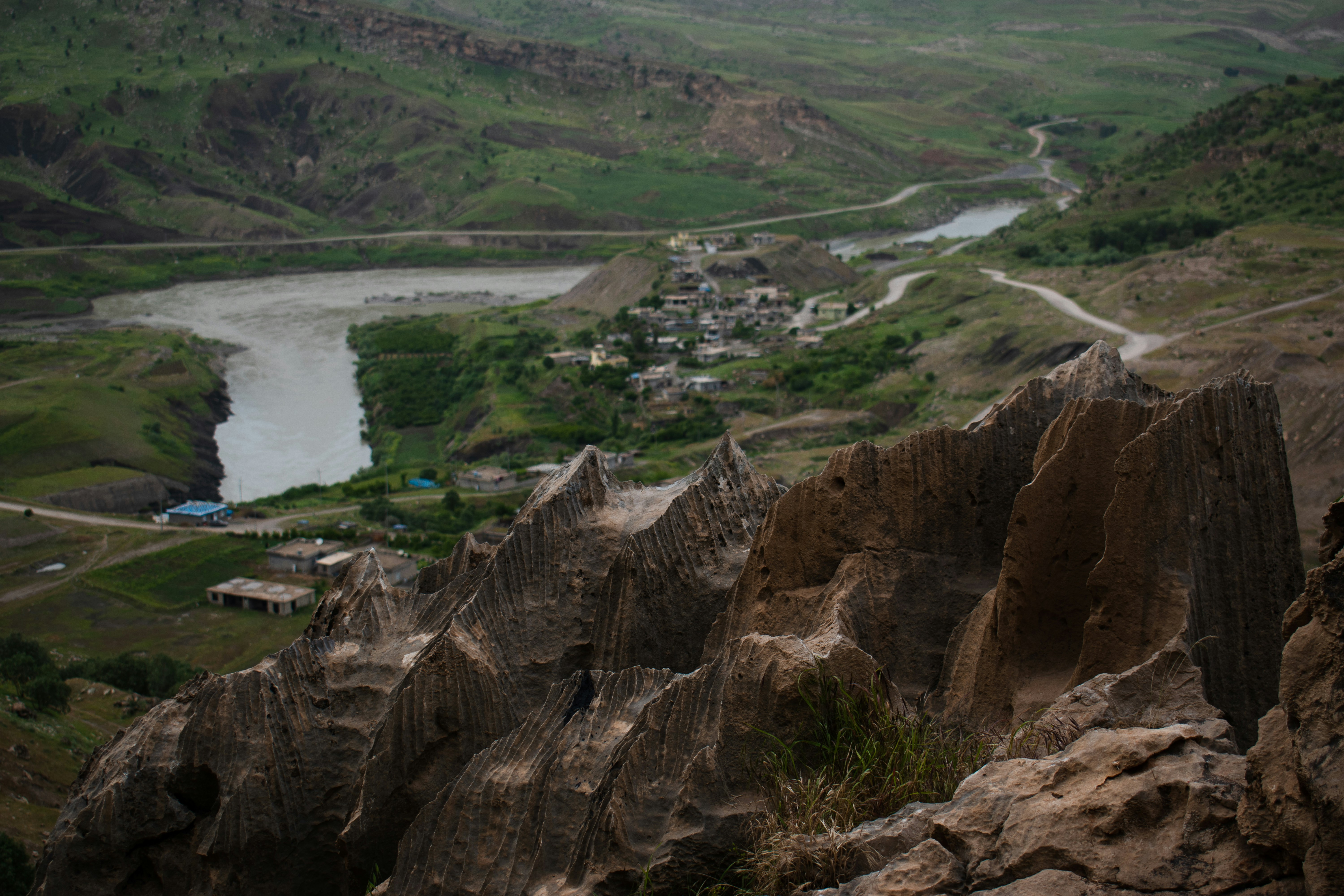 Jagged rock formations overlook a winding river and a small village nestled in the lush valley below.