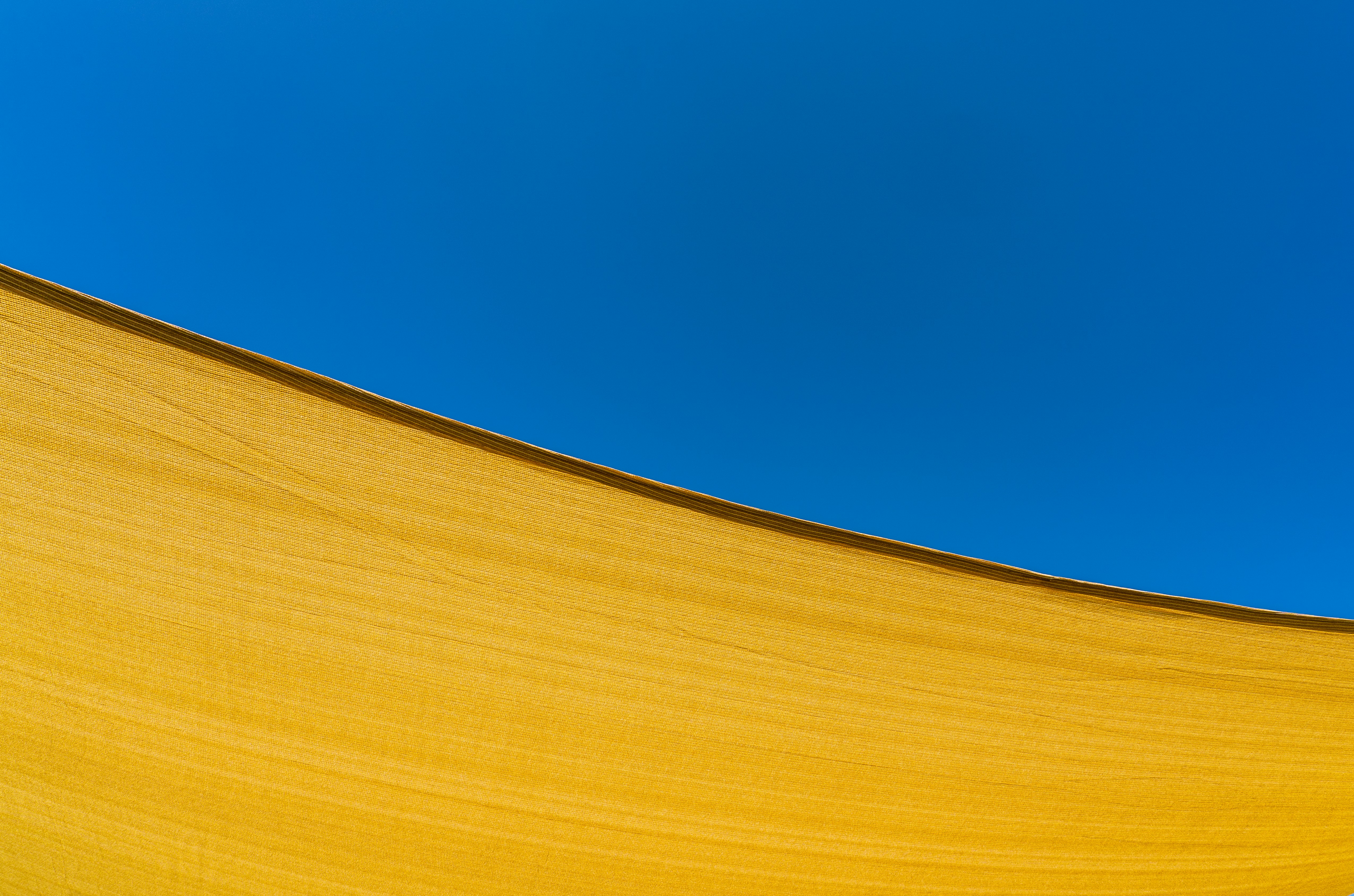 Curved yellow fabric against a clear blue sky, creating a striking contrast and minimalist composition.