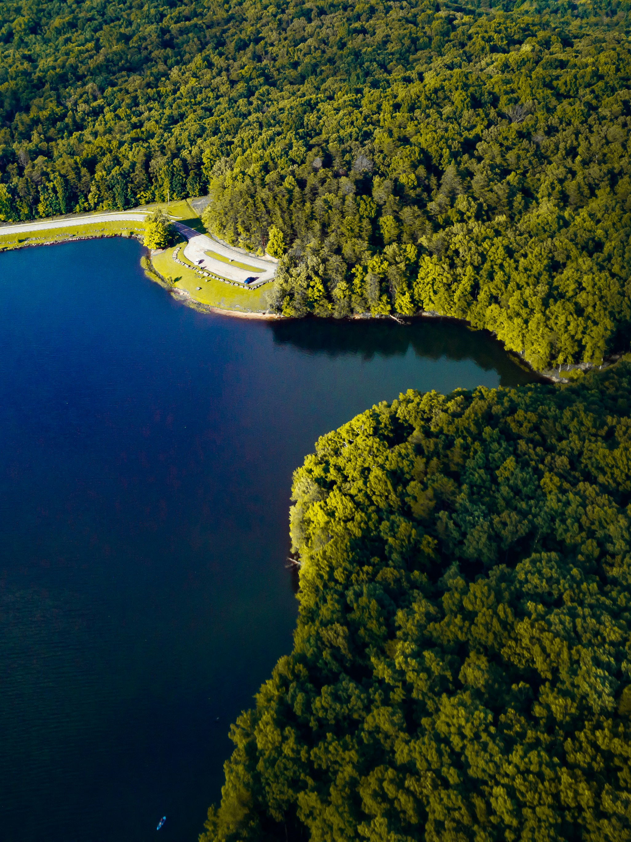 Aerial view of a tranquil lake bordered by dense green forests, featuring a small building along the shoreline.