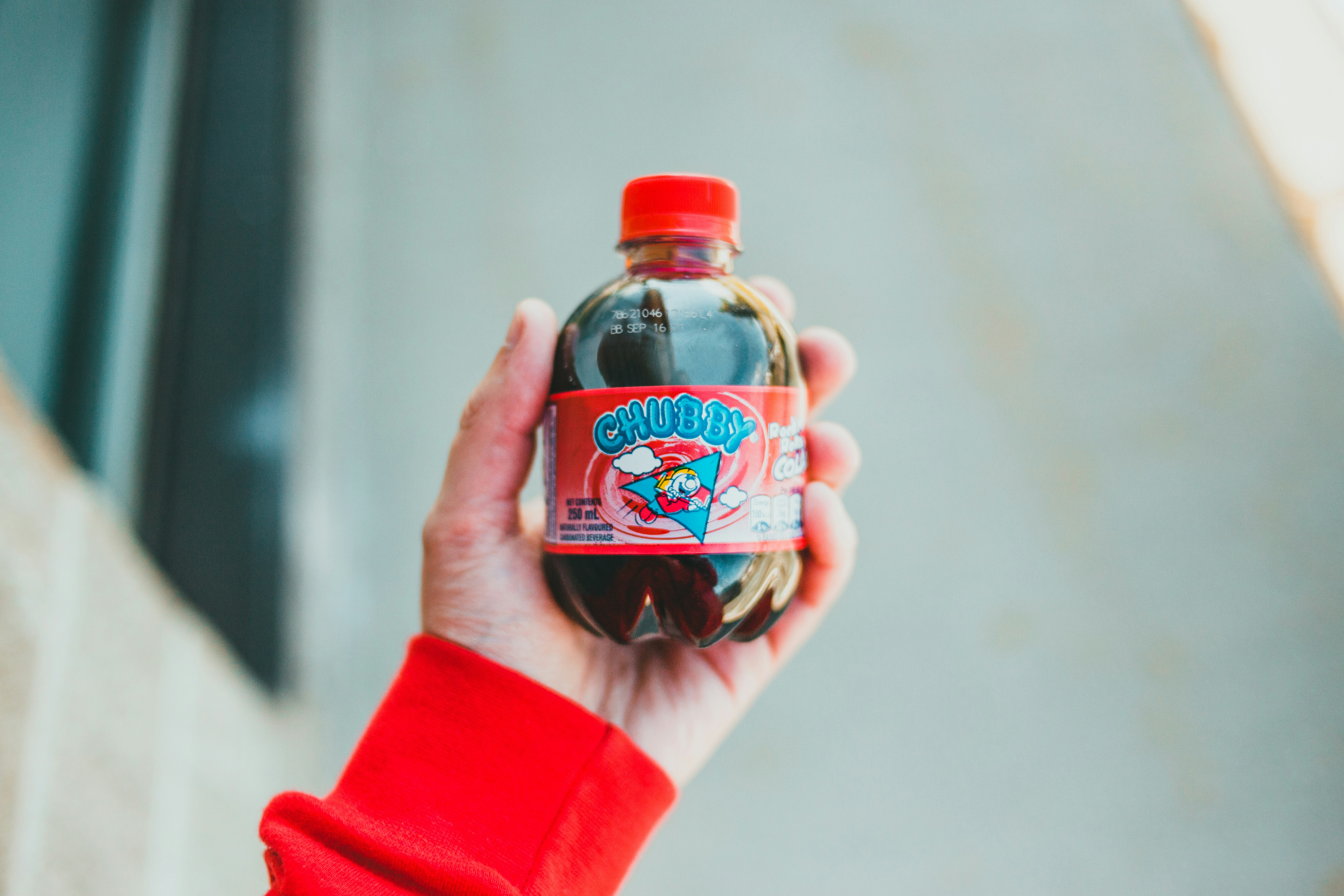 Bottle of Chubby Cola: Bright Red Sleeve, Bold Label, Handheld Adrift in City Light