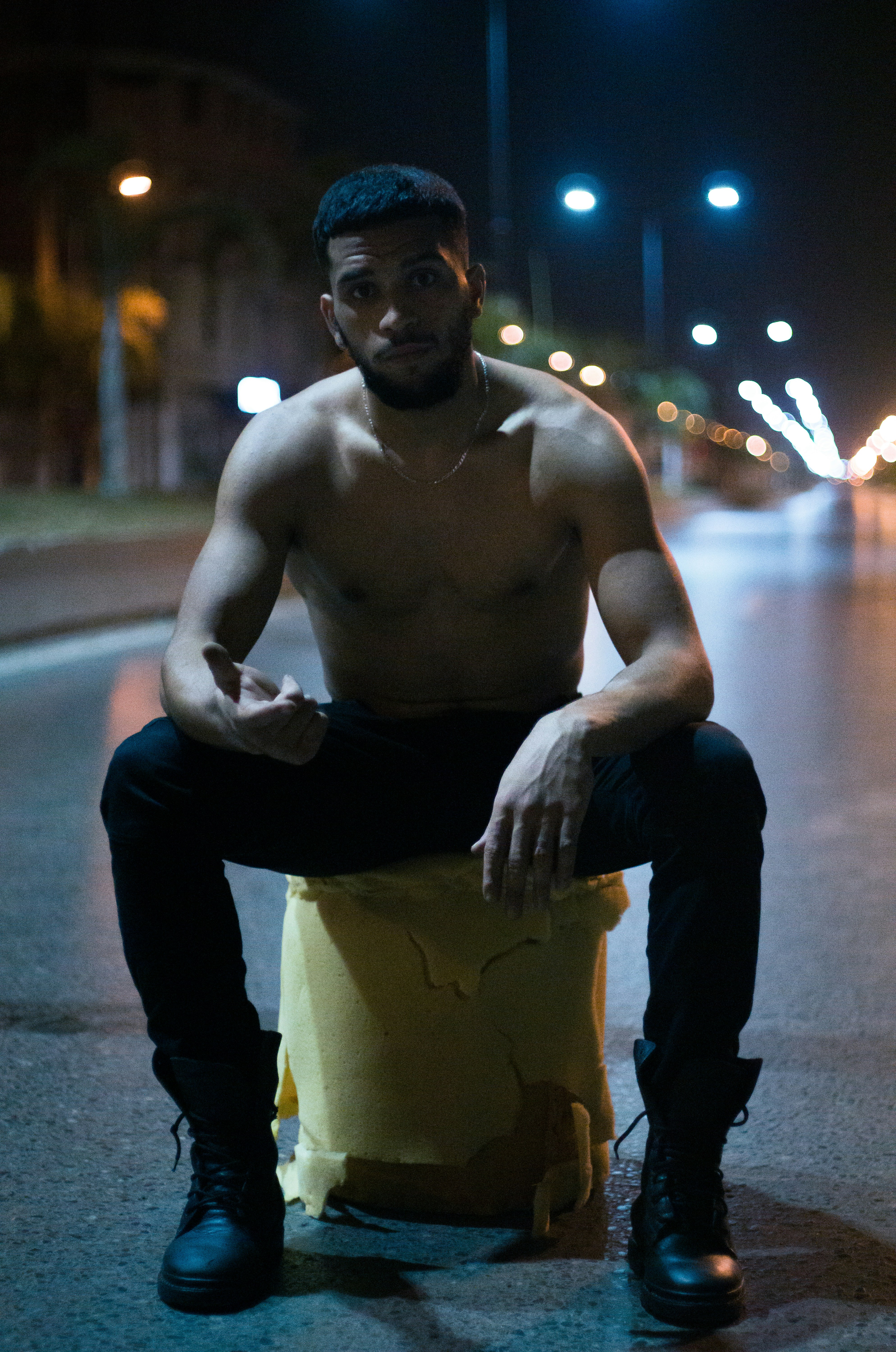 Midnight Grit: A shirtless figure perched on a yellow block under neon streetlights