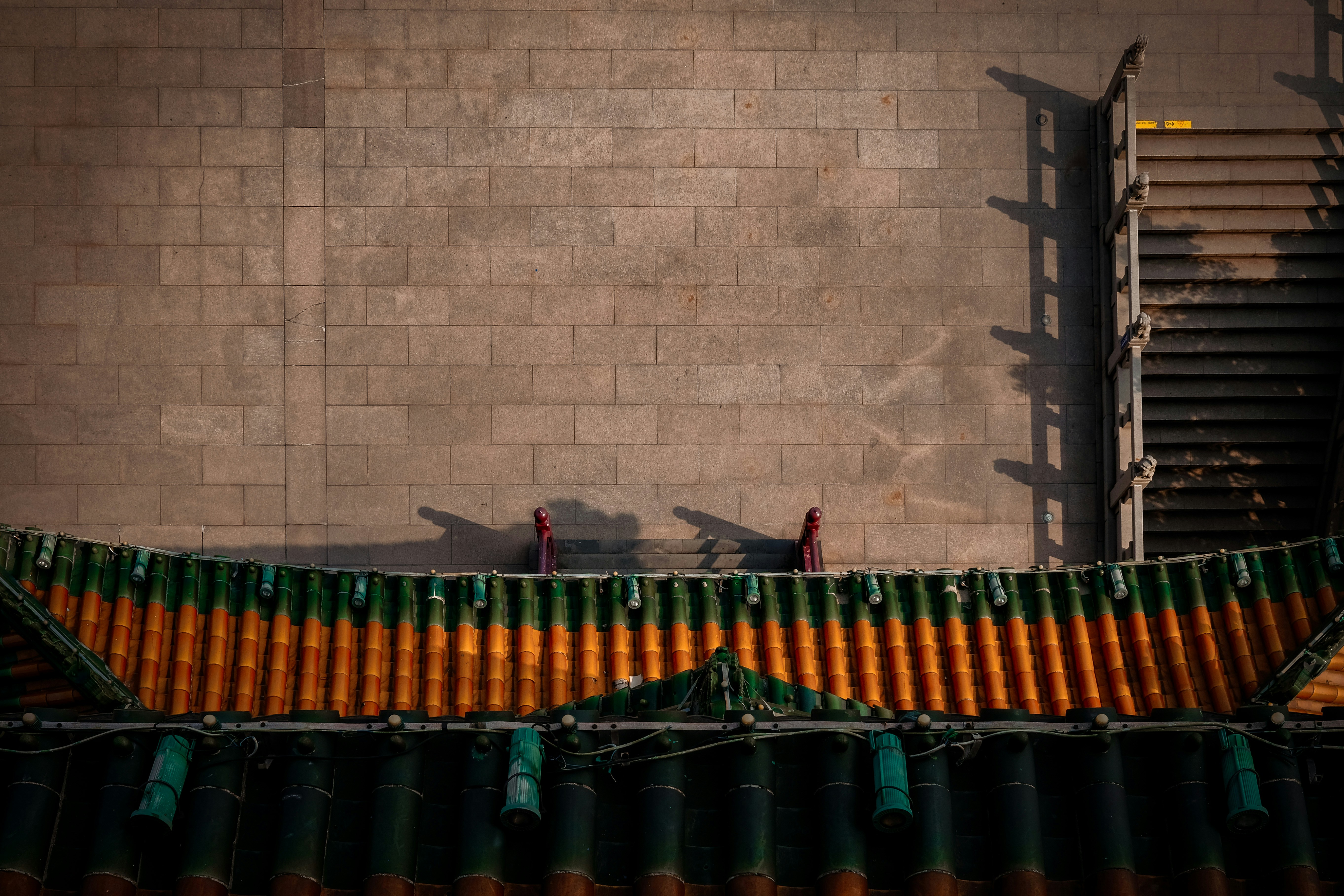Colorful tiled rooftop casting shadows on a sunlit stone wall.