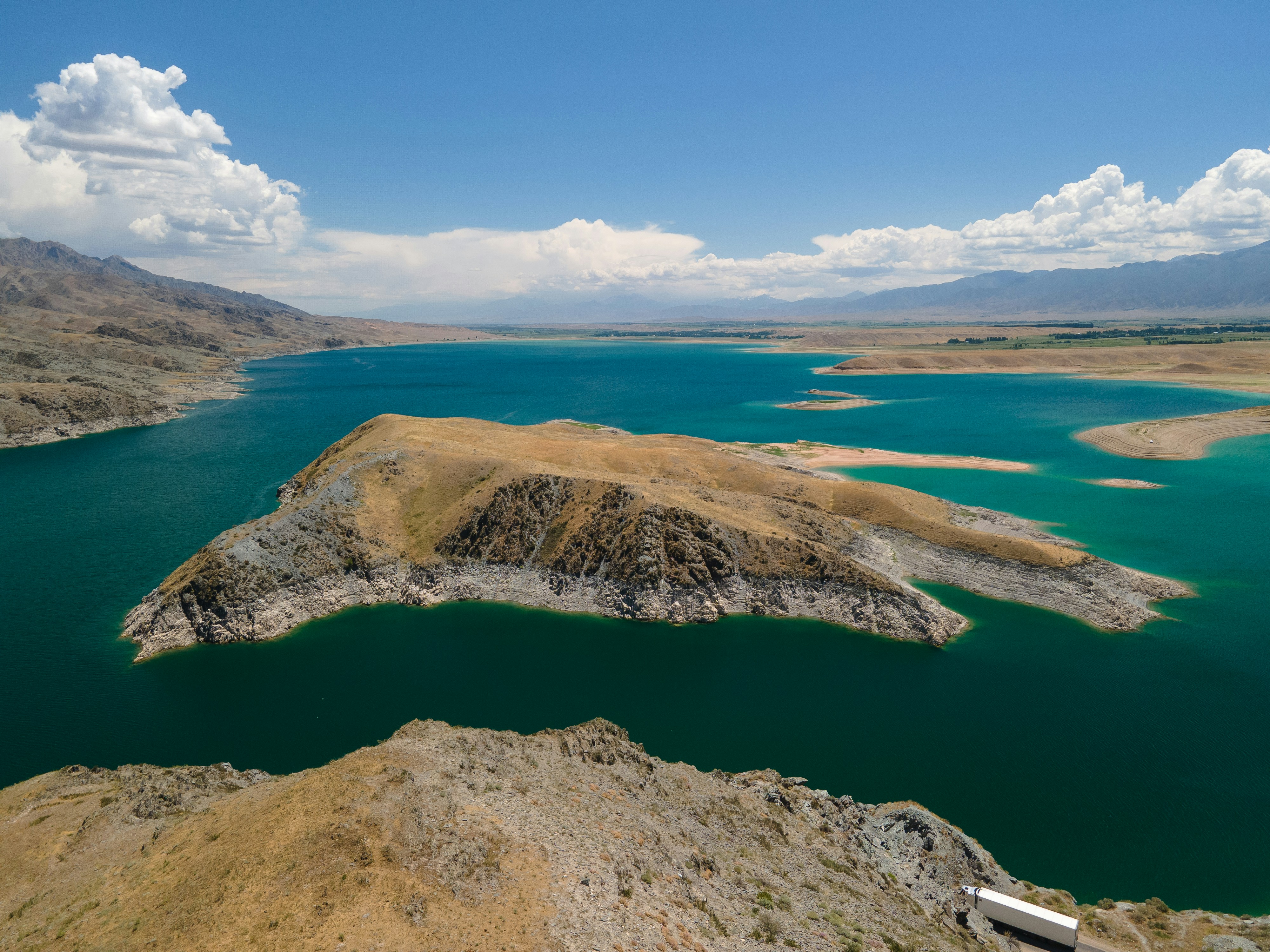 Brown and green mountains surrounding a vibrant blue reservoir under a clear sky.