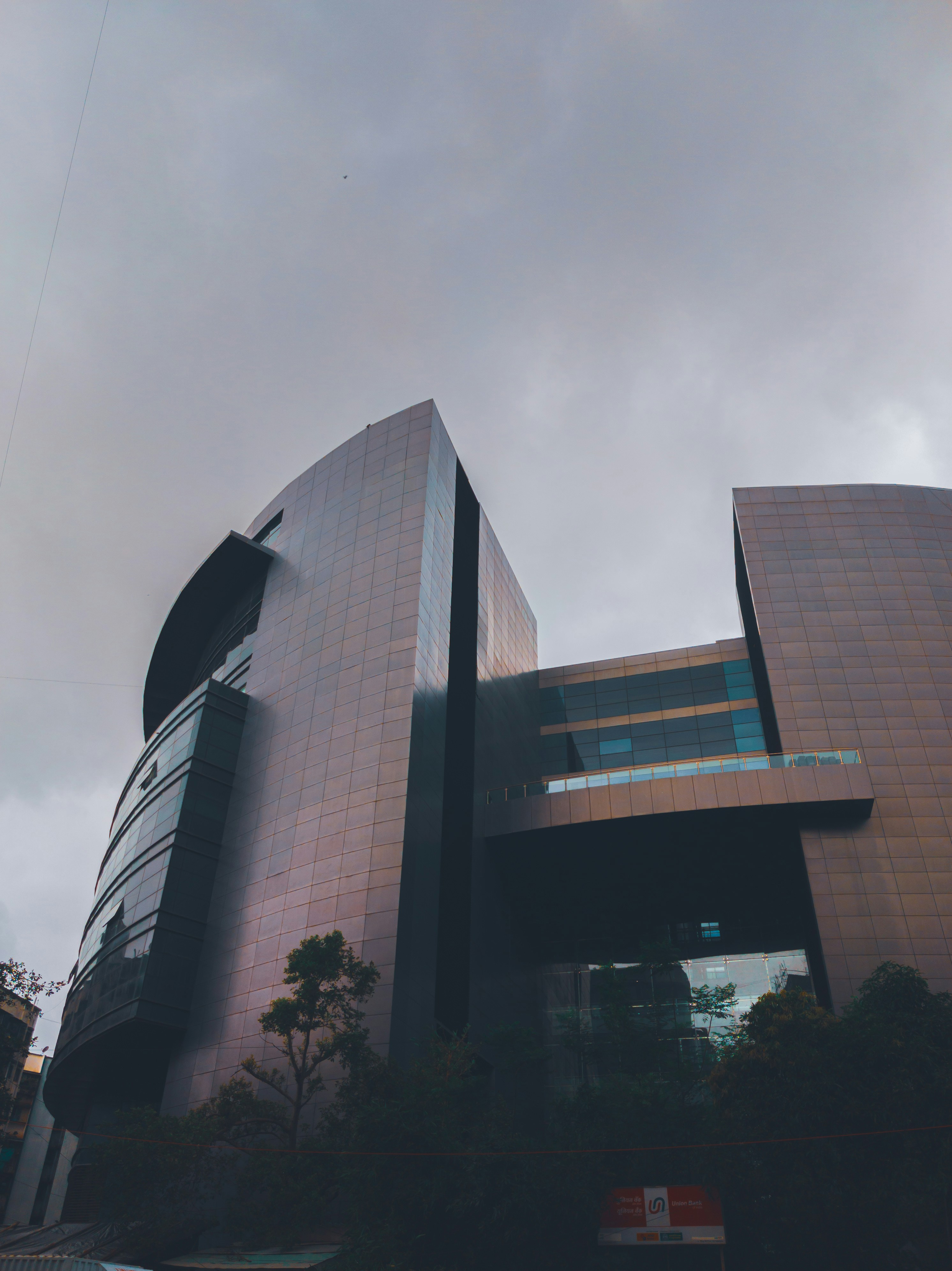 Modern building with sleek glass and metallic surfaces, contrasting against a moody sky. The structure showcases innovative architectural design.