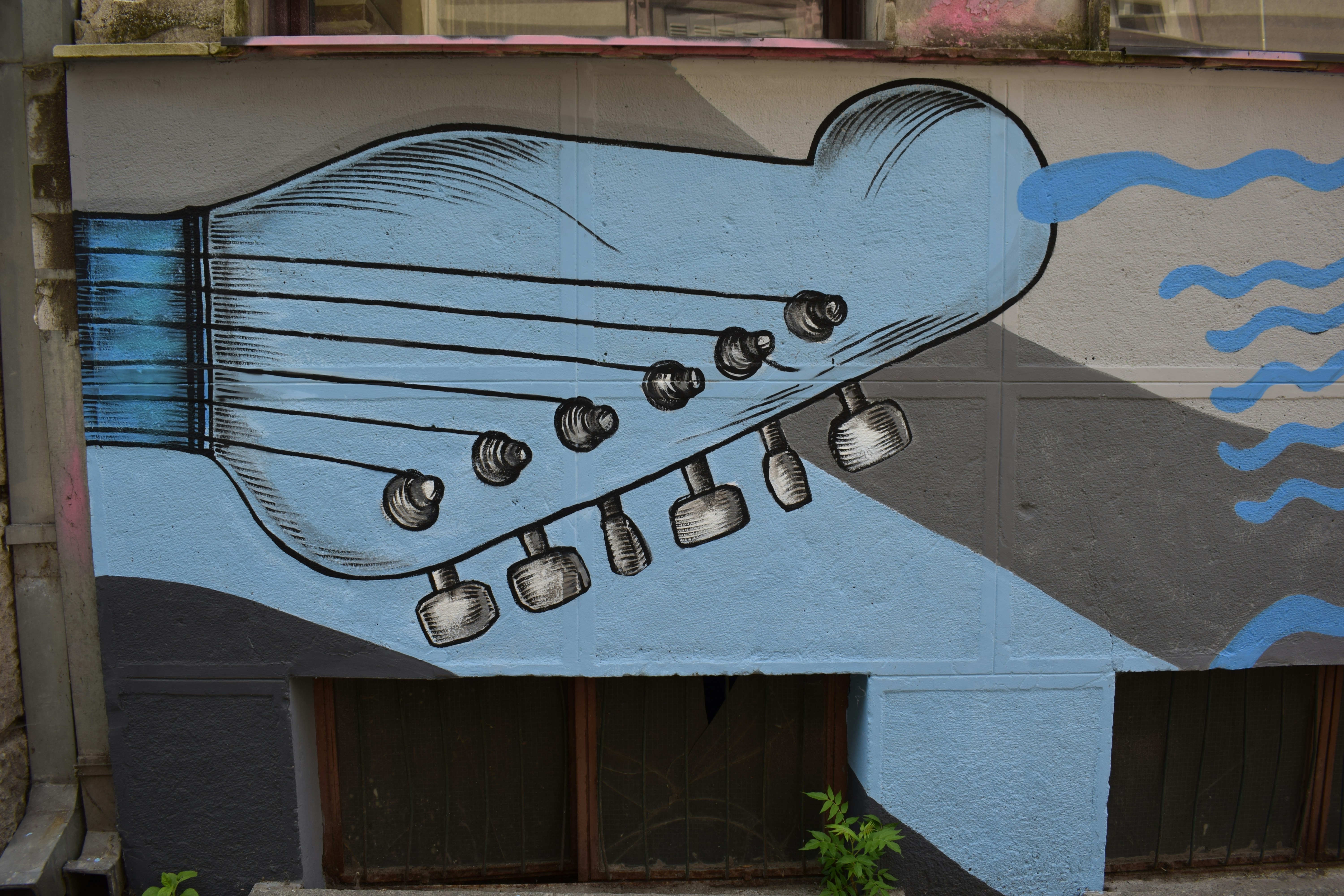 A vibrant mural depicting the headstock of a guitar, blending artistic expression with urban architecture. The blue tones and intricate details evoke a musical theme.