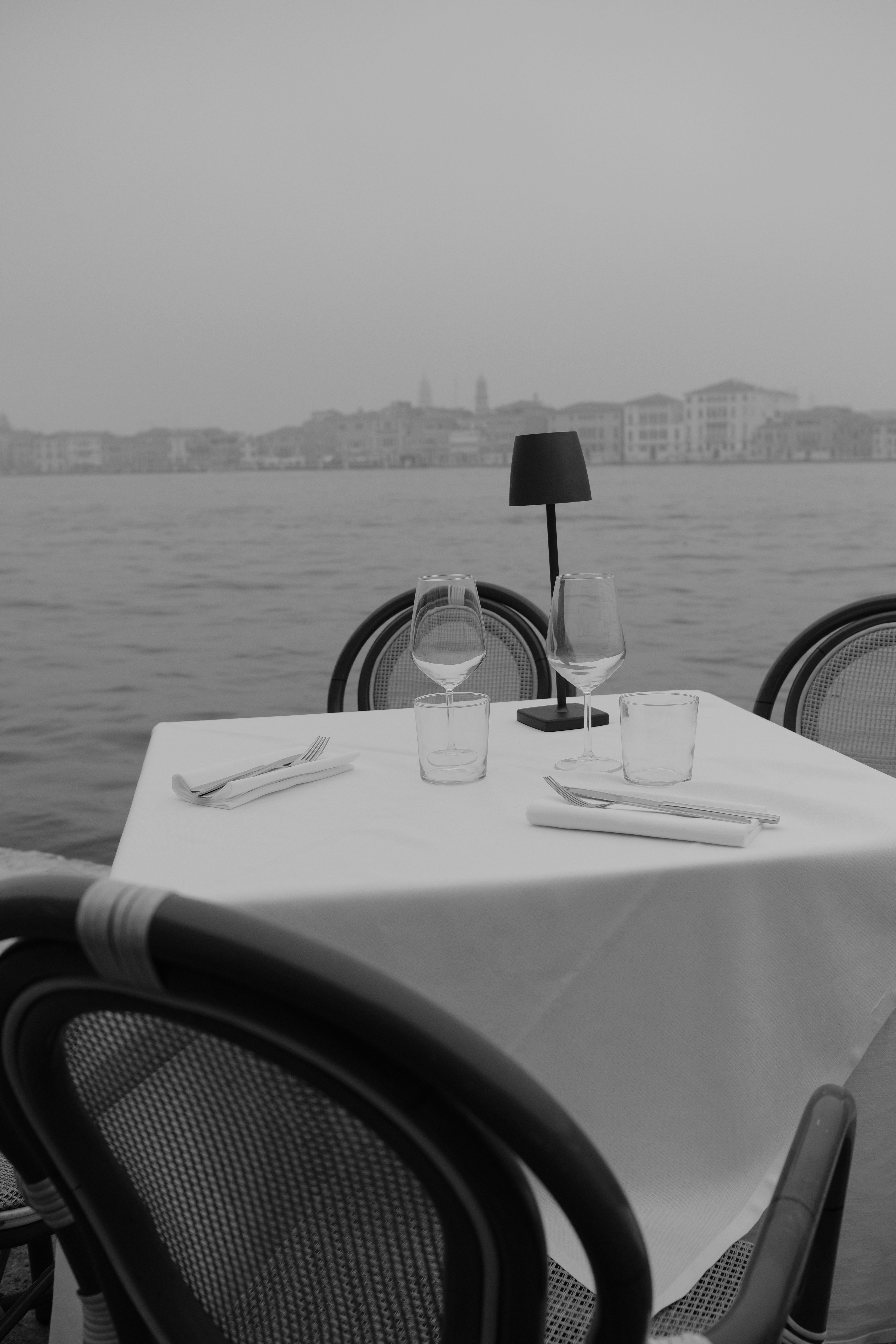 Monochrome Harbor Table: Glassware and Lamp Beside a Distant City