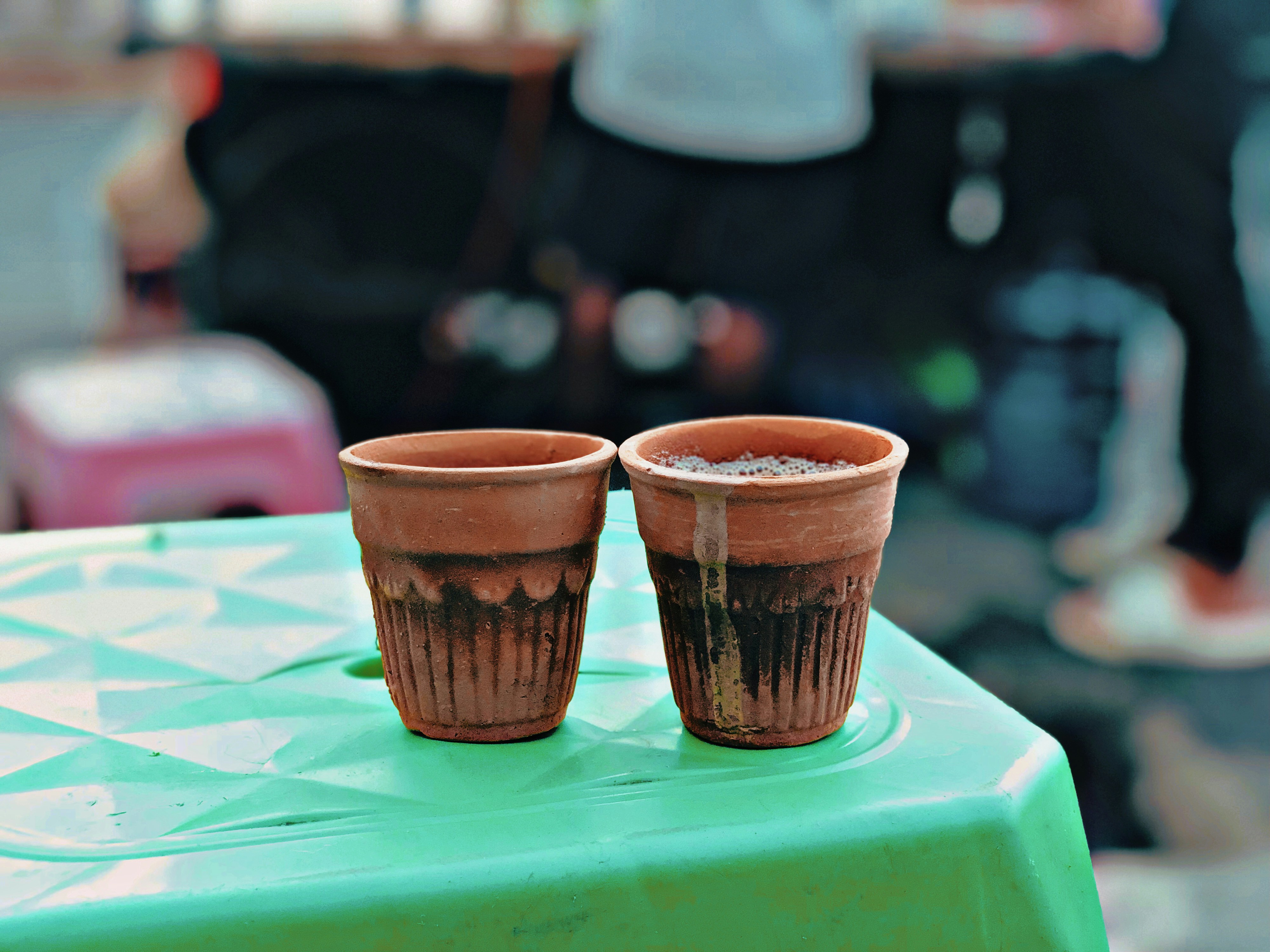 Two rustic terracotta pots resting on a vibrant green surface, hinting at a gardening theme. Soil is visible in one pot, suggesting preparation for planting.
