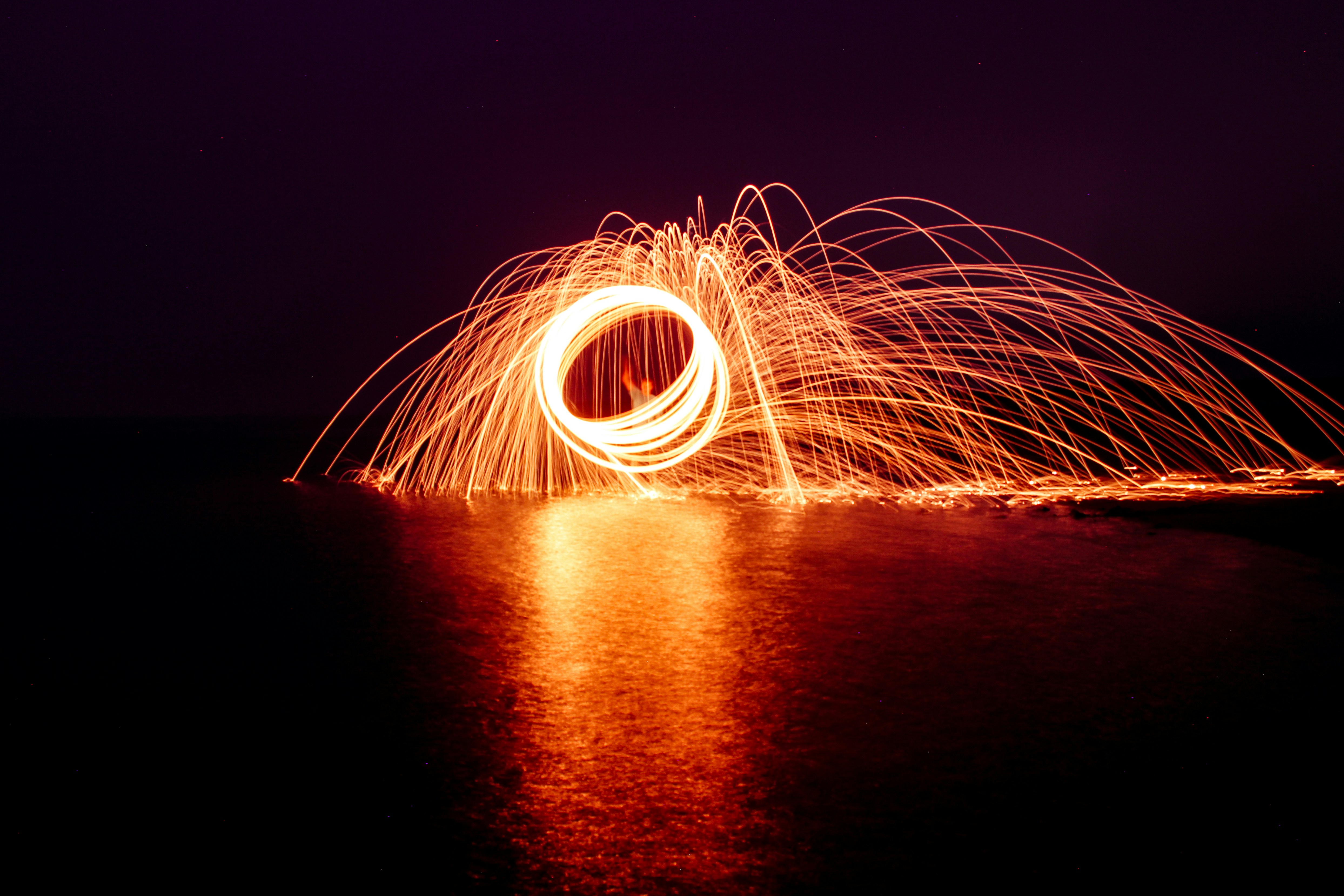 steel wool photography of person standing on body of water during night time