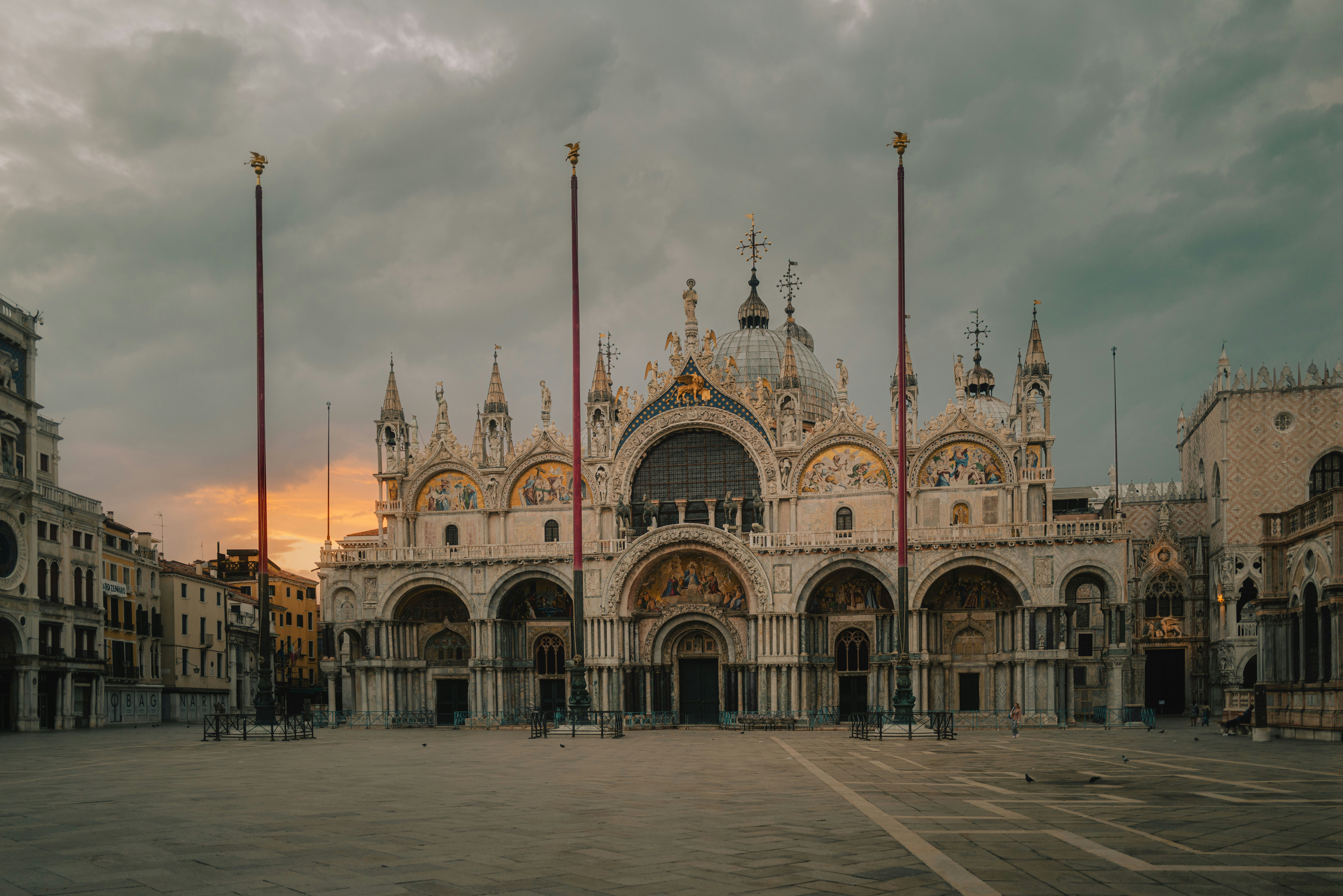 Intricate façade of St. Mark's Basilica illuminated by the setting sun, with towering columns framing the scene.