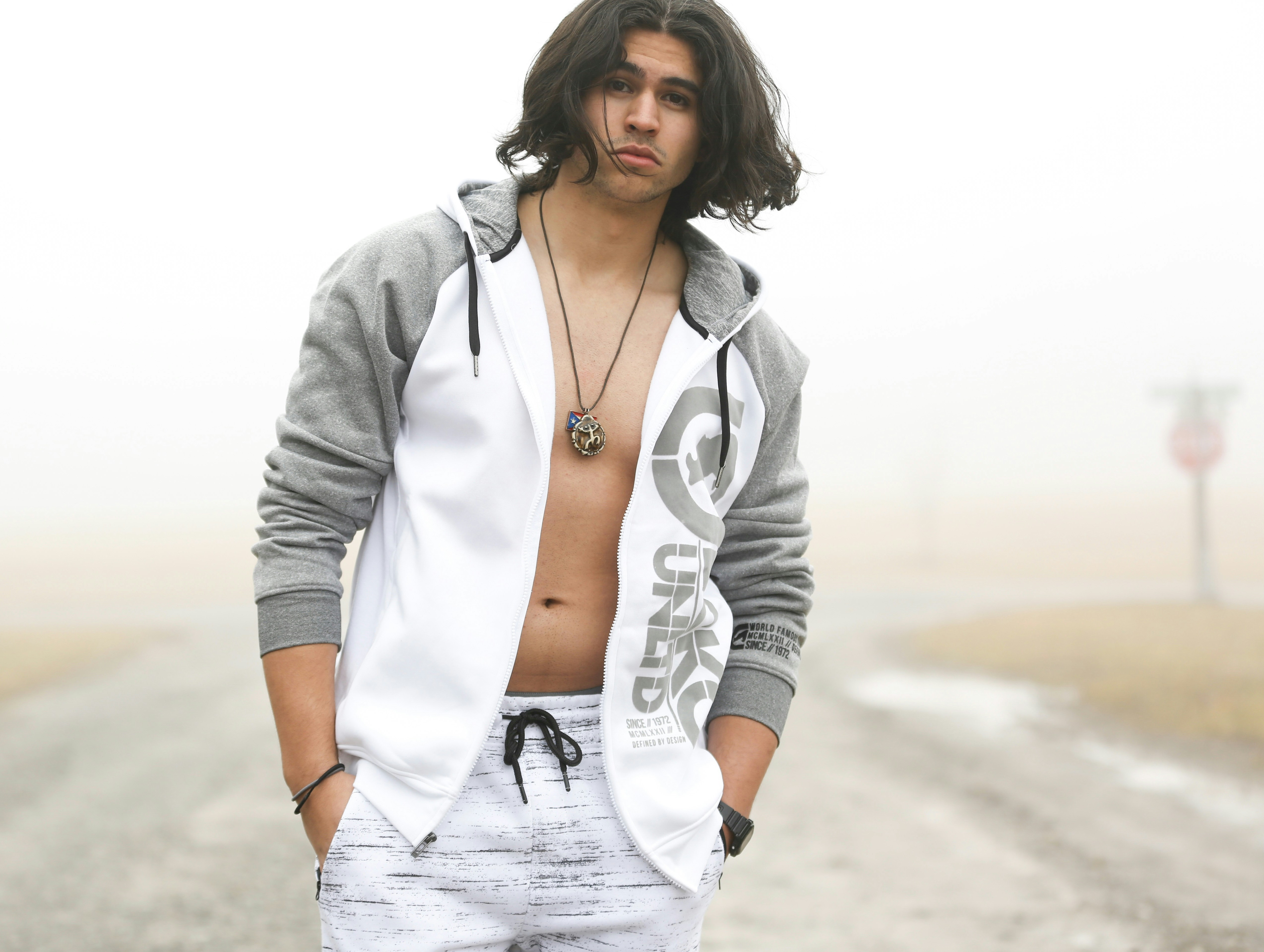 Young man in a stylish hoodie stands confidently on a foggy road, exuding a sense of calm amidst the haze.