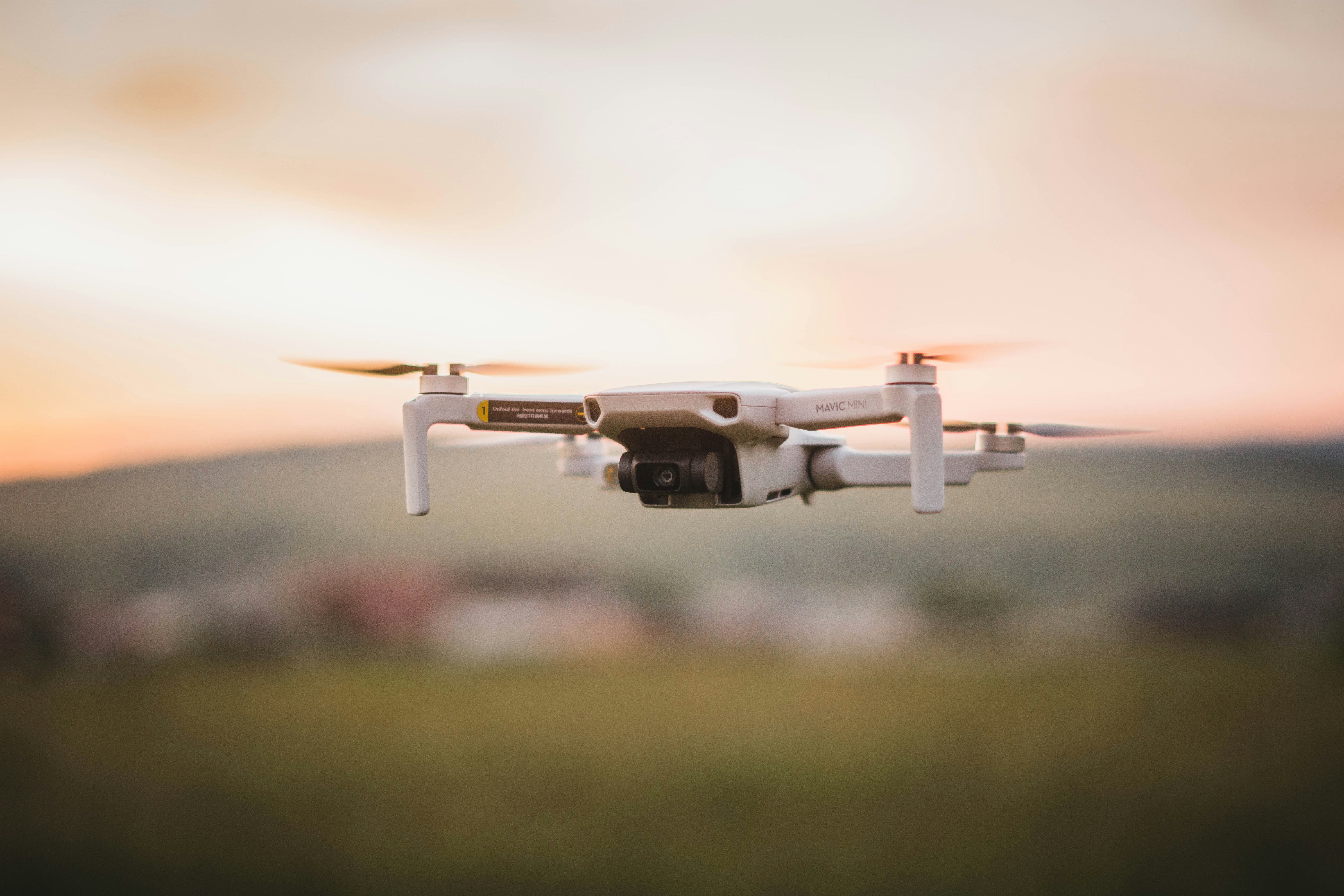 A drone hovers gracefully against a soft, pastel sunset sky, showcasing its sleek design and advanced technology.