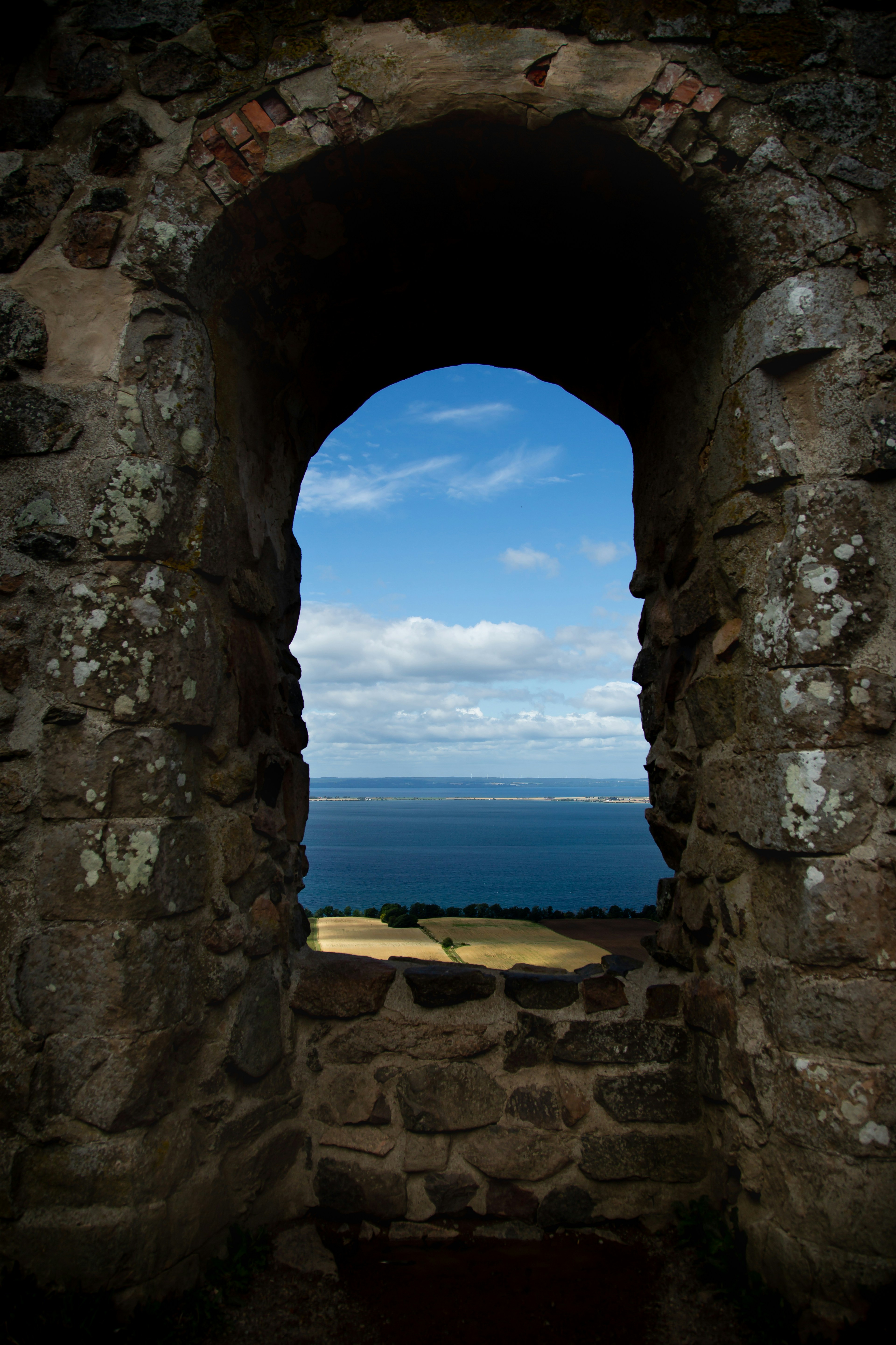Stone archway revealing a tranquil seascape under a dynamic sky. The view invites contemplation of nature's beauty.