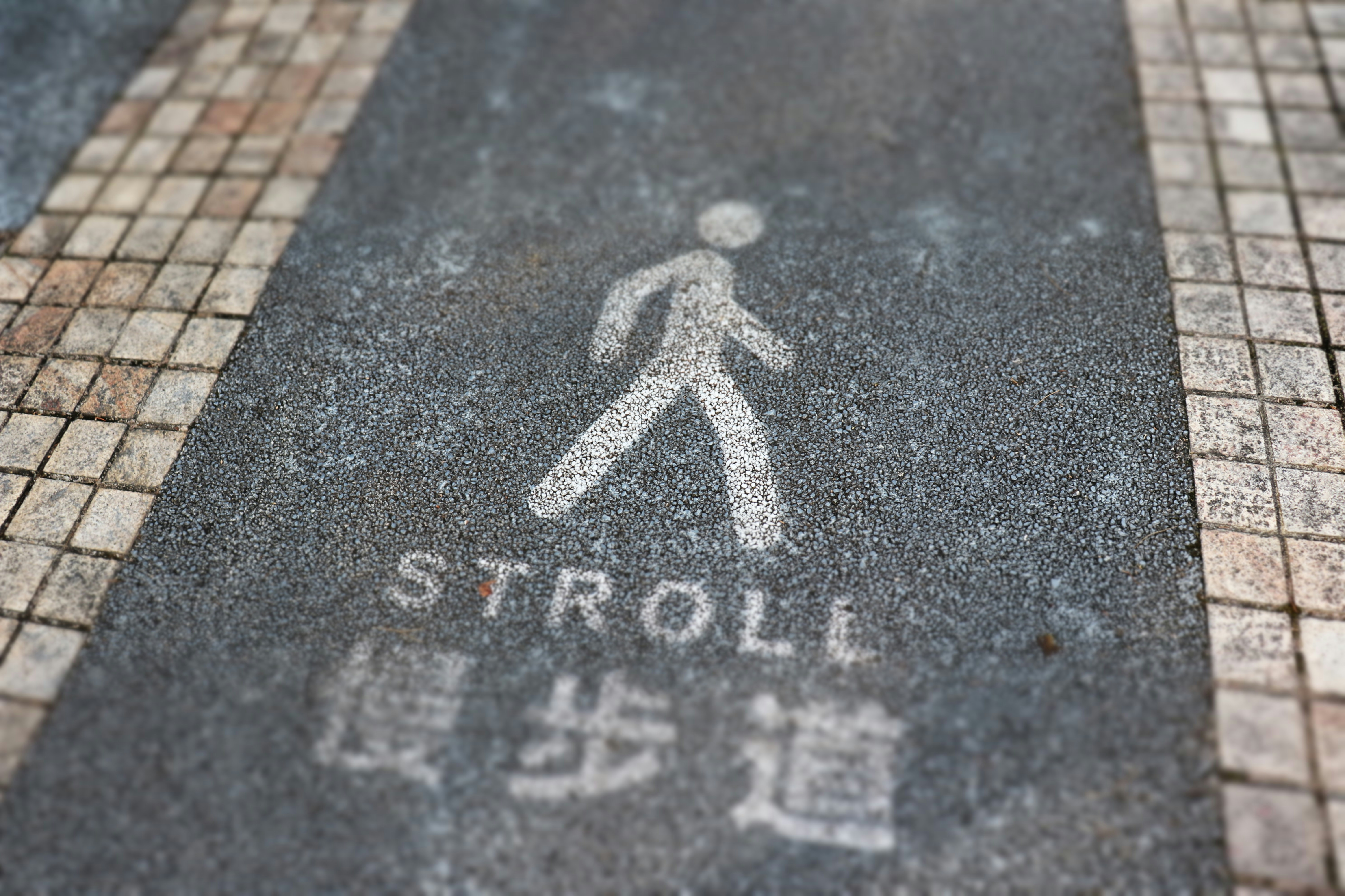 Sidewalk stencil indicating a pedestrian path with the word 'STROLL' in English and Chinese characters. The design emphasizes walkability in urban settings.