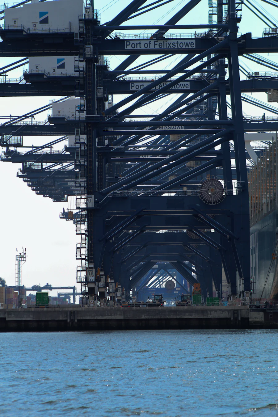 Multiple blue gantry cranes extend in a repeating tunnel toward the dock, creating a perspective corridor above calm water.