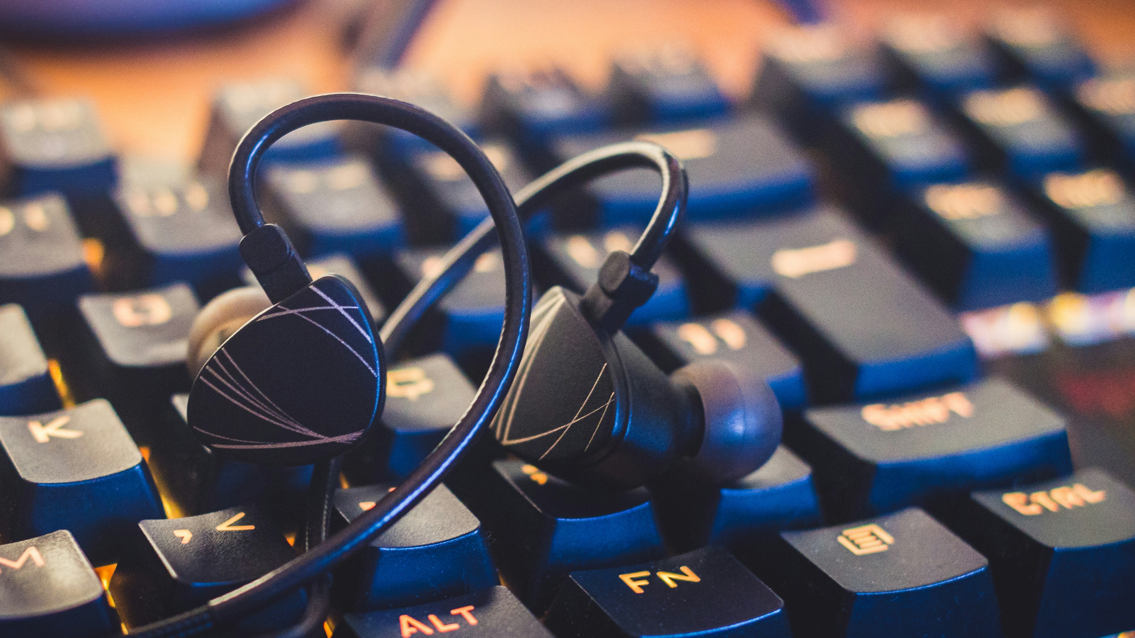 In-ear monitors resting on a computer keyboard under warm lighting.