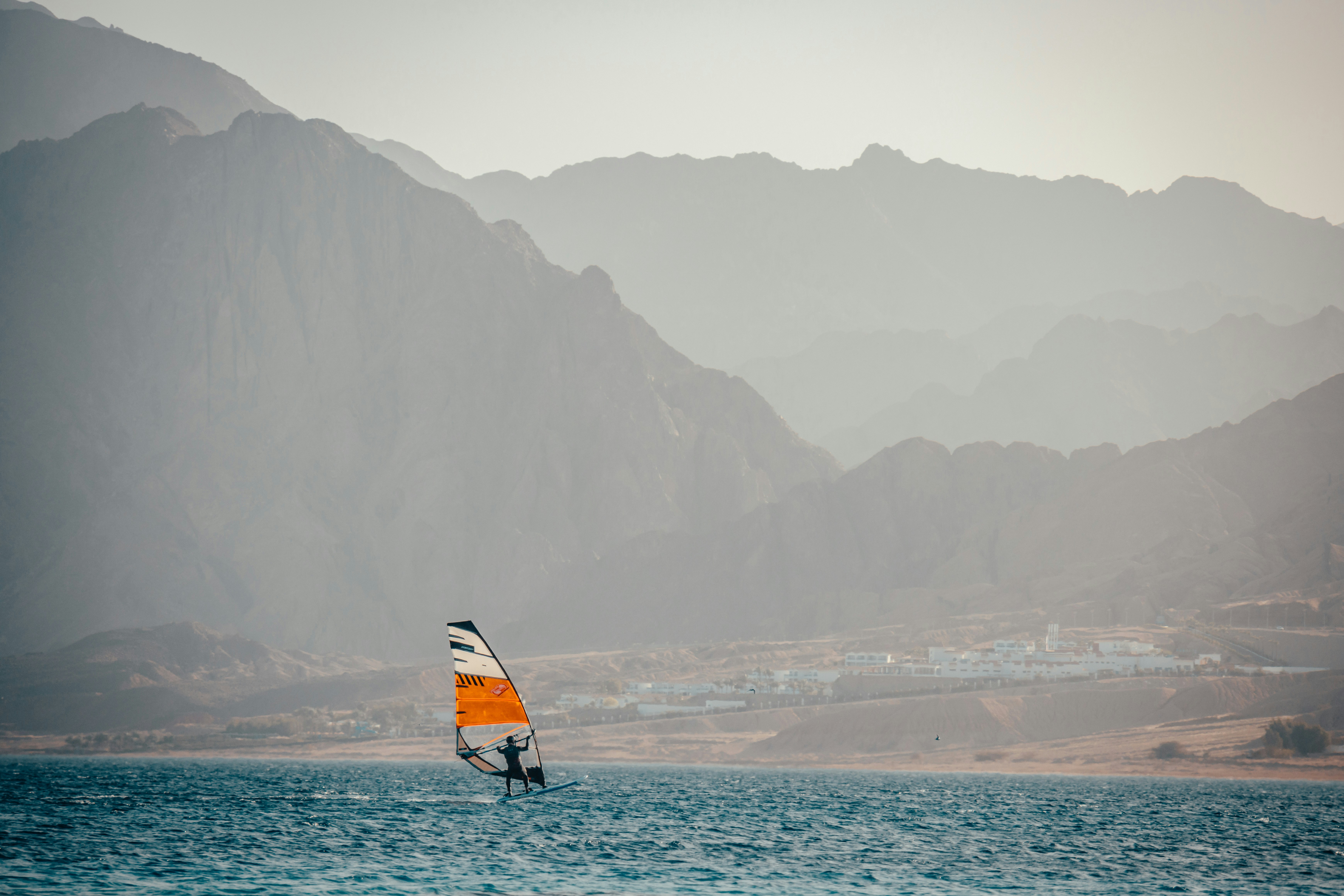 Wind-chased Dawn: Windsurfer Skims a Misty Sea Beneath Quiet Peaks