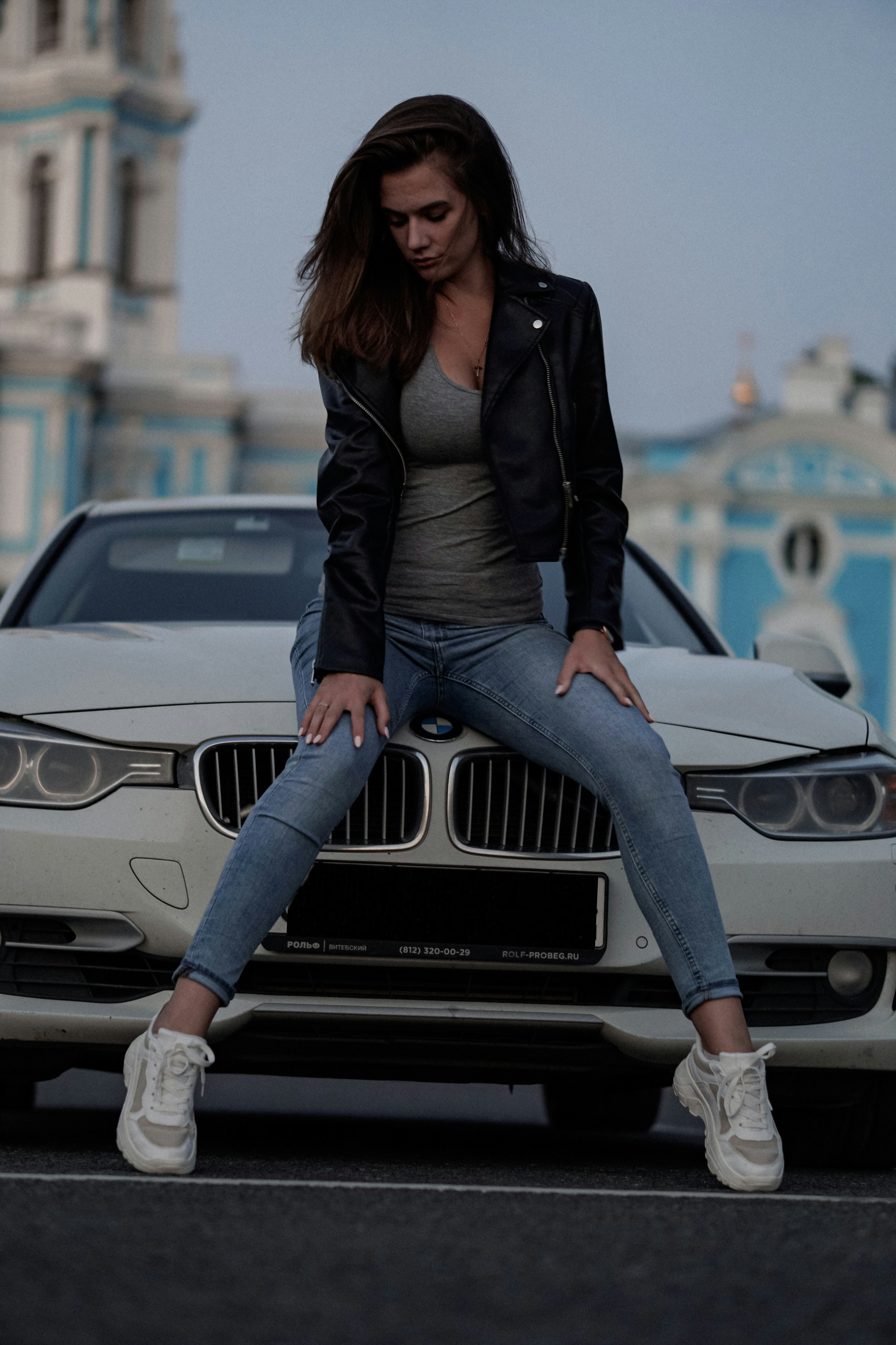 Woman in black leather jacket and blue denim jeans sitting on white ...