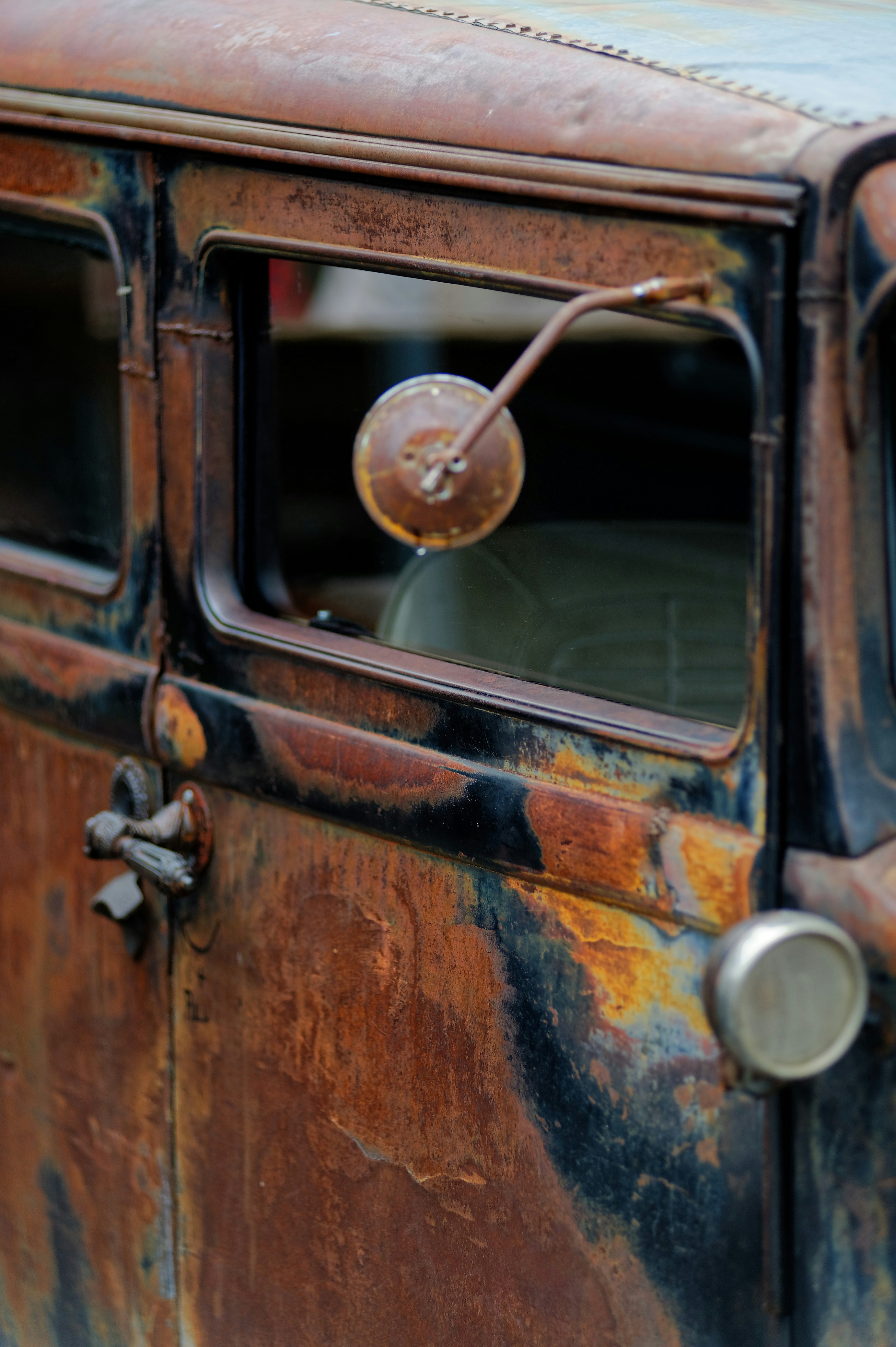Close-up of a weathered vintage car door showcasing rust patterns and an antique side mirror. The worn textures tell a story of age and nostalgia.