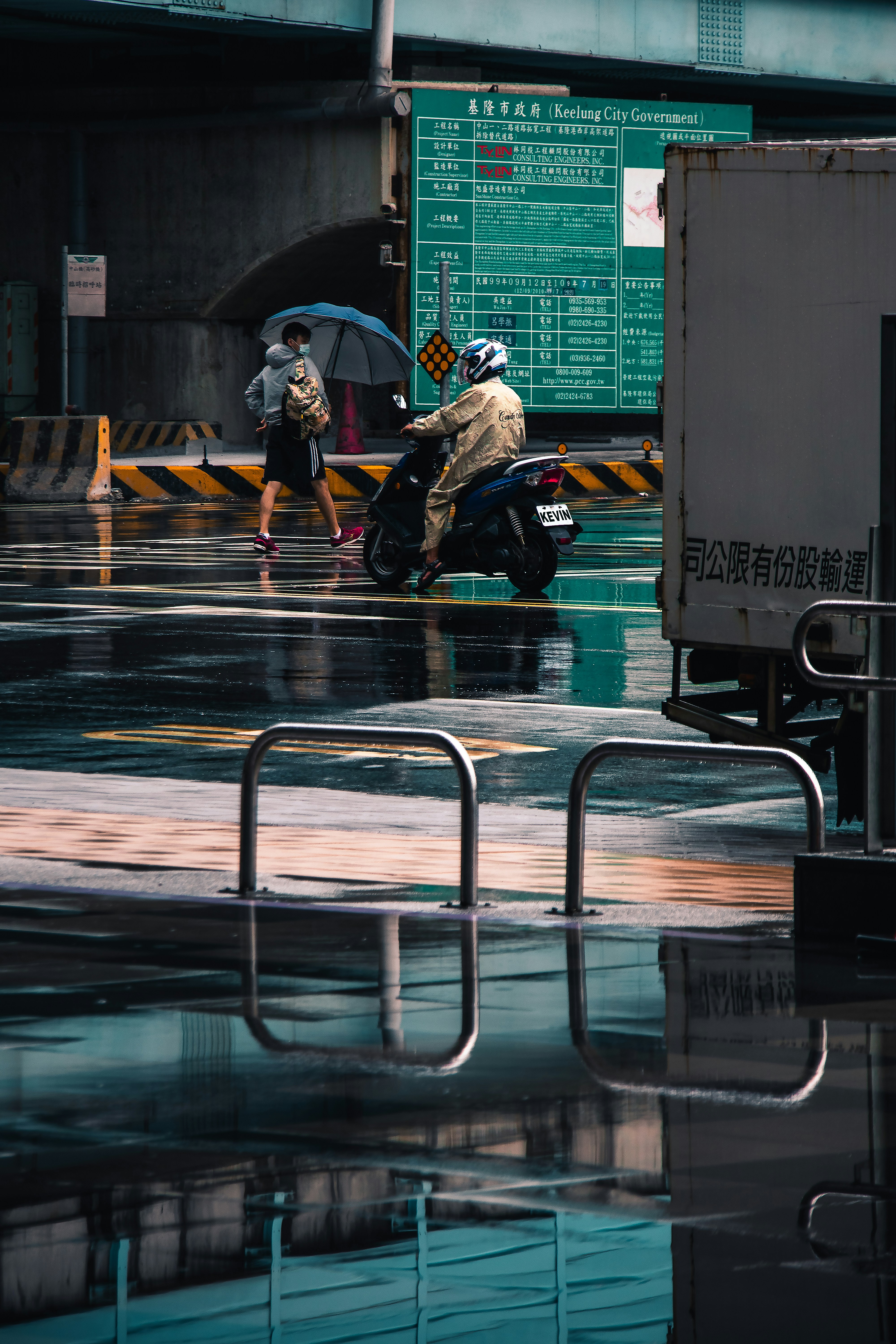 Rain-Slick Intersection: Scooter Rider Paired with Umbrella in Front of a Green City Sign