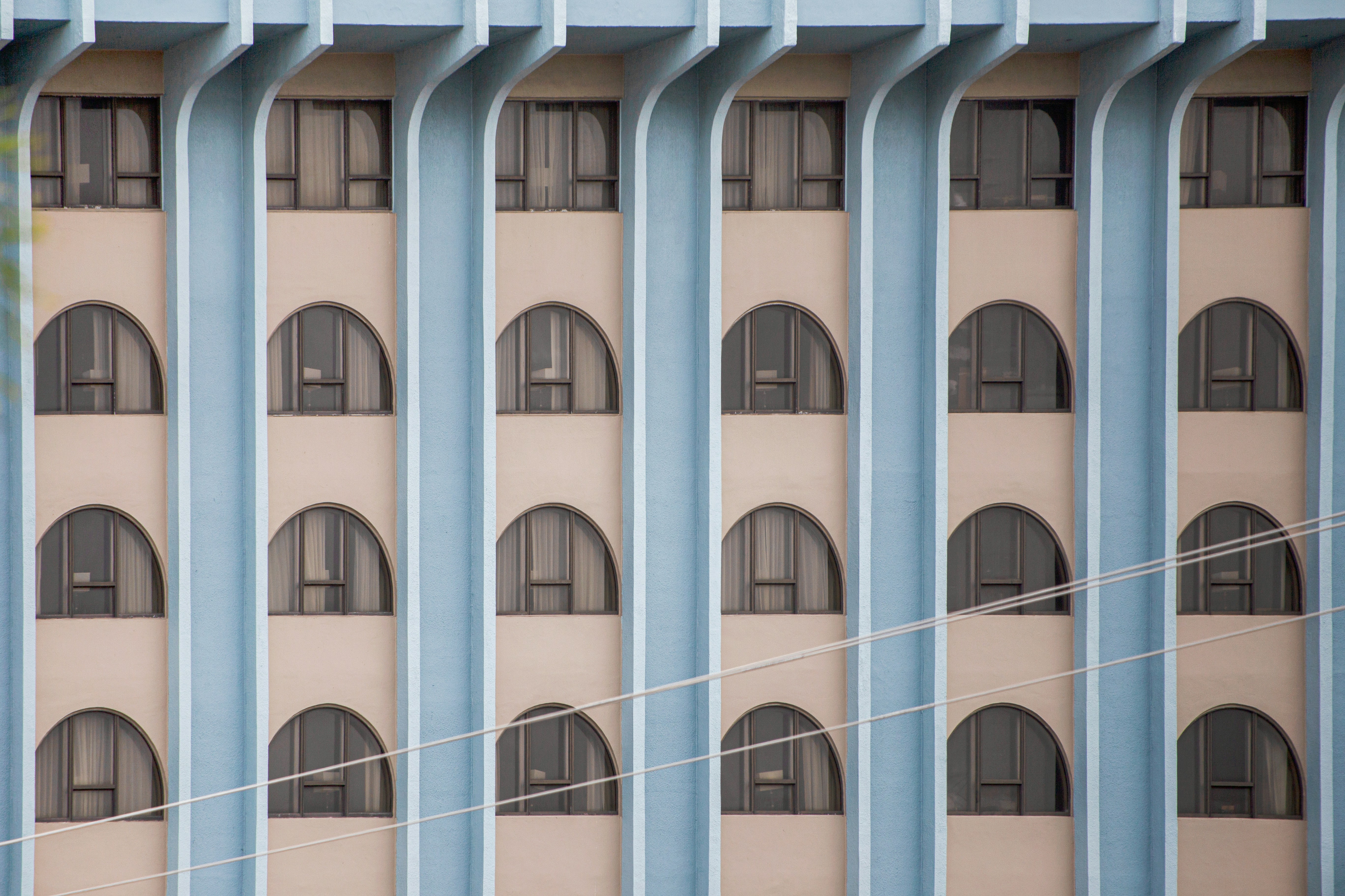 Close-up of a building facade featuring a rhythmic pattern of arched windows framed by blue and beige tones. The design showcases a blend of modern architecture with classic elements.