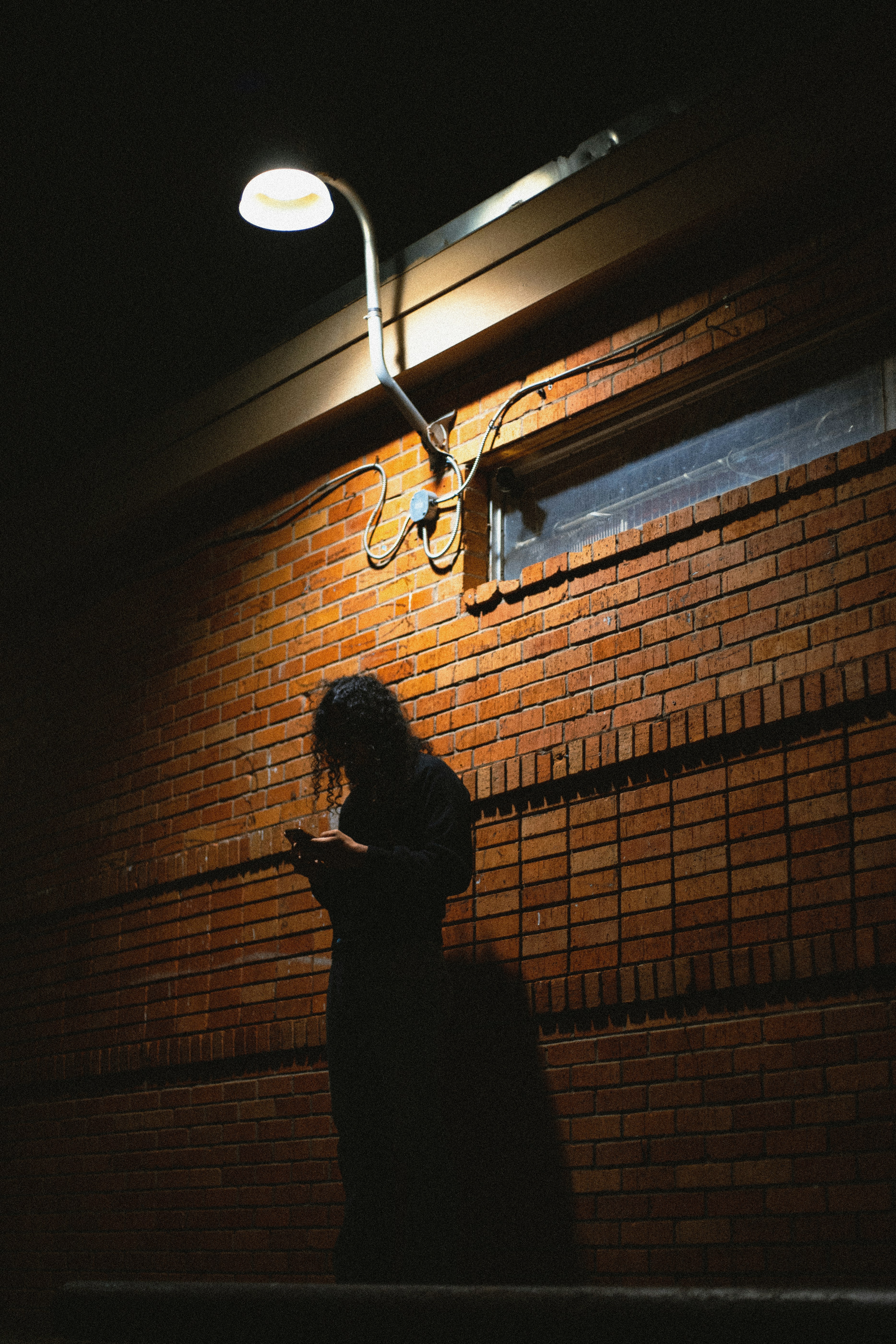 Lone Silhouette by the Brick Wall under a Quiet Streetlamp